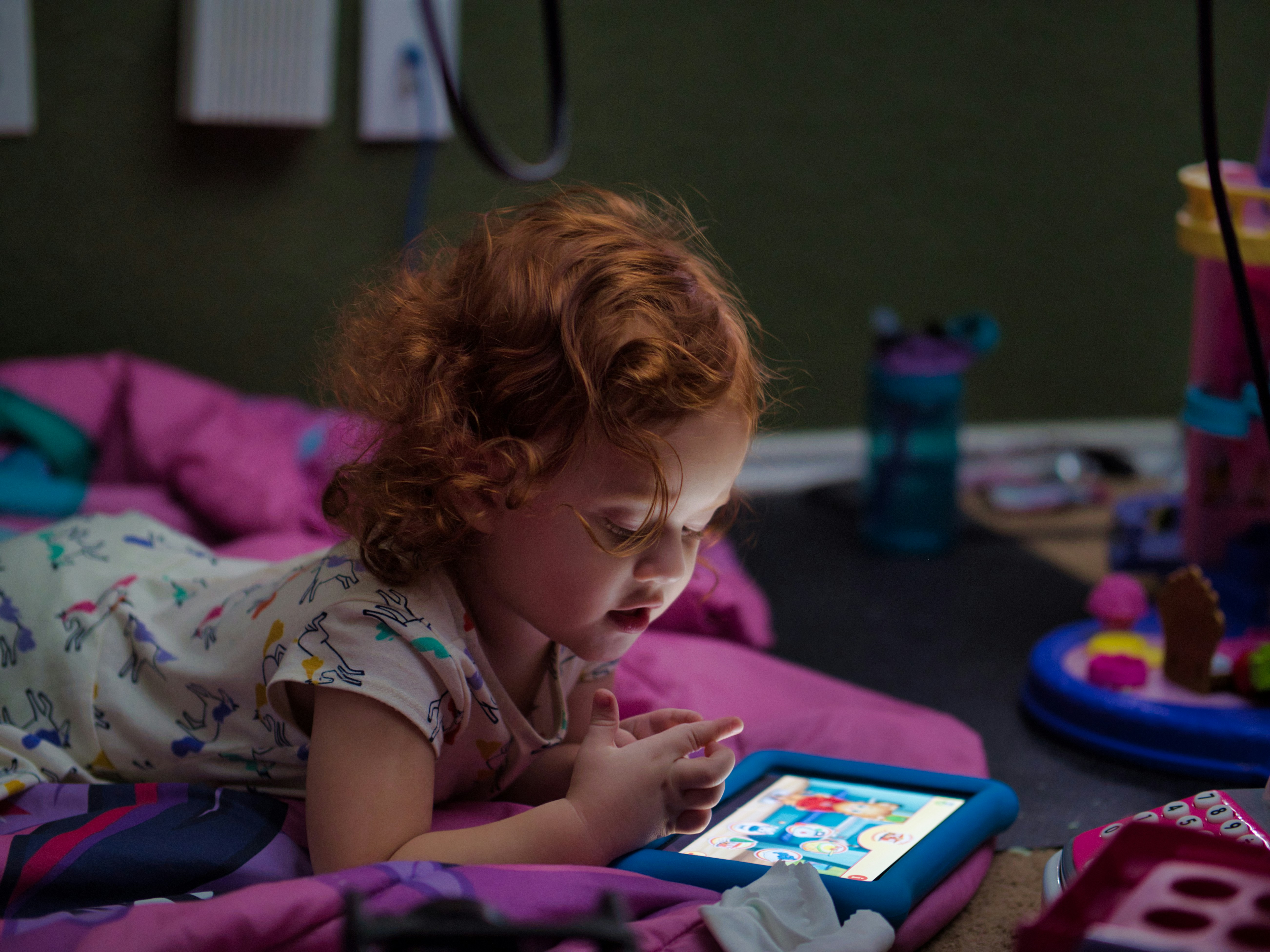 Little girl with curly red hair focused on a tablet.