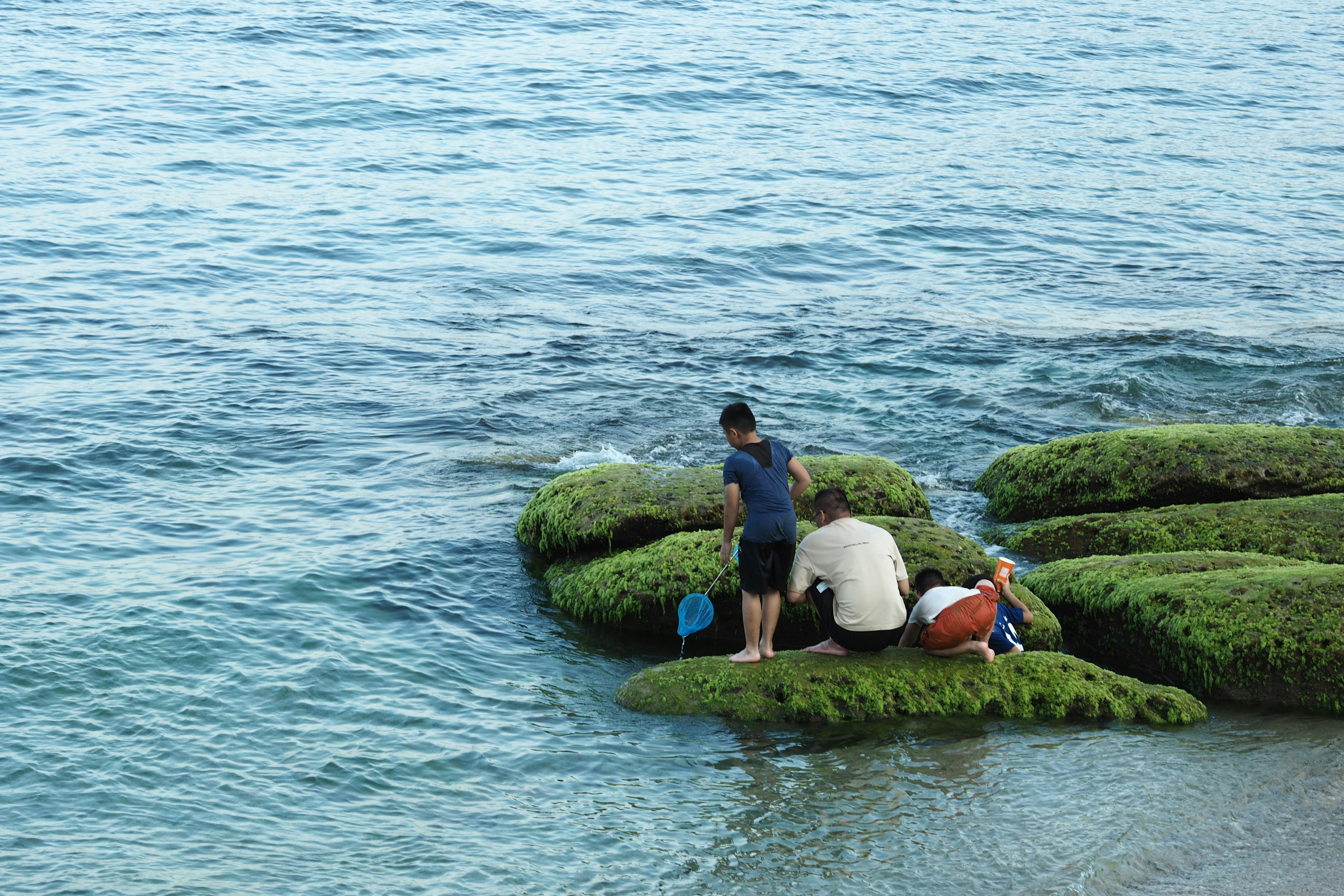 West Shore Picnic: Three Figures Resting on Moss-Covered Rocks