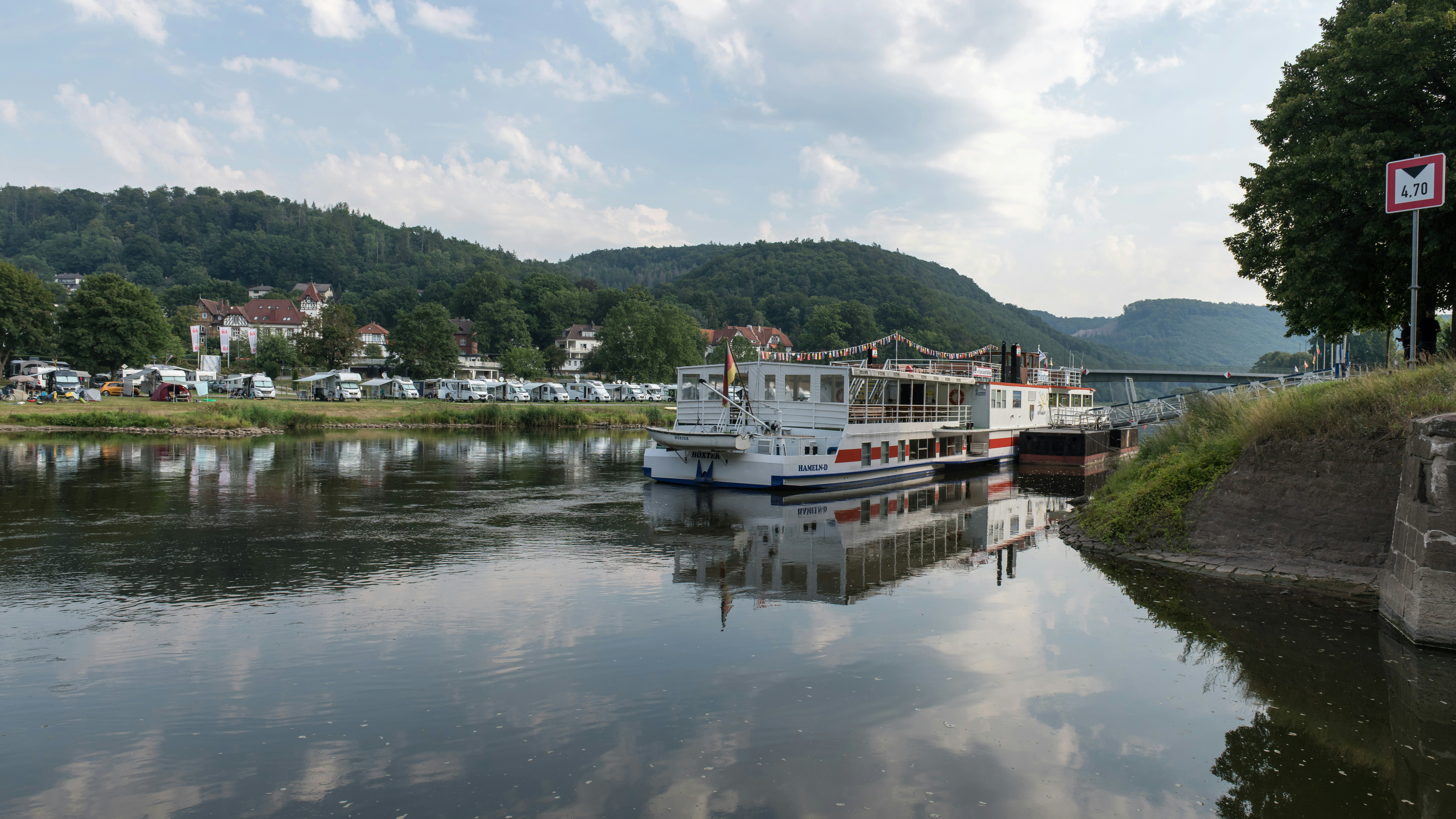 A white paddle steamer docked on a river with hills.