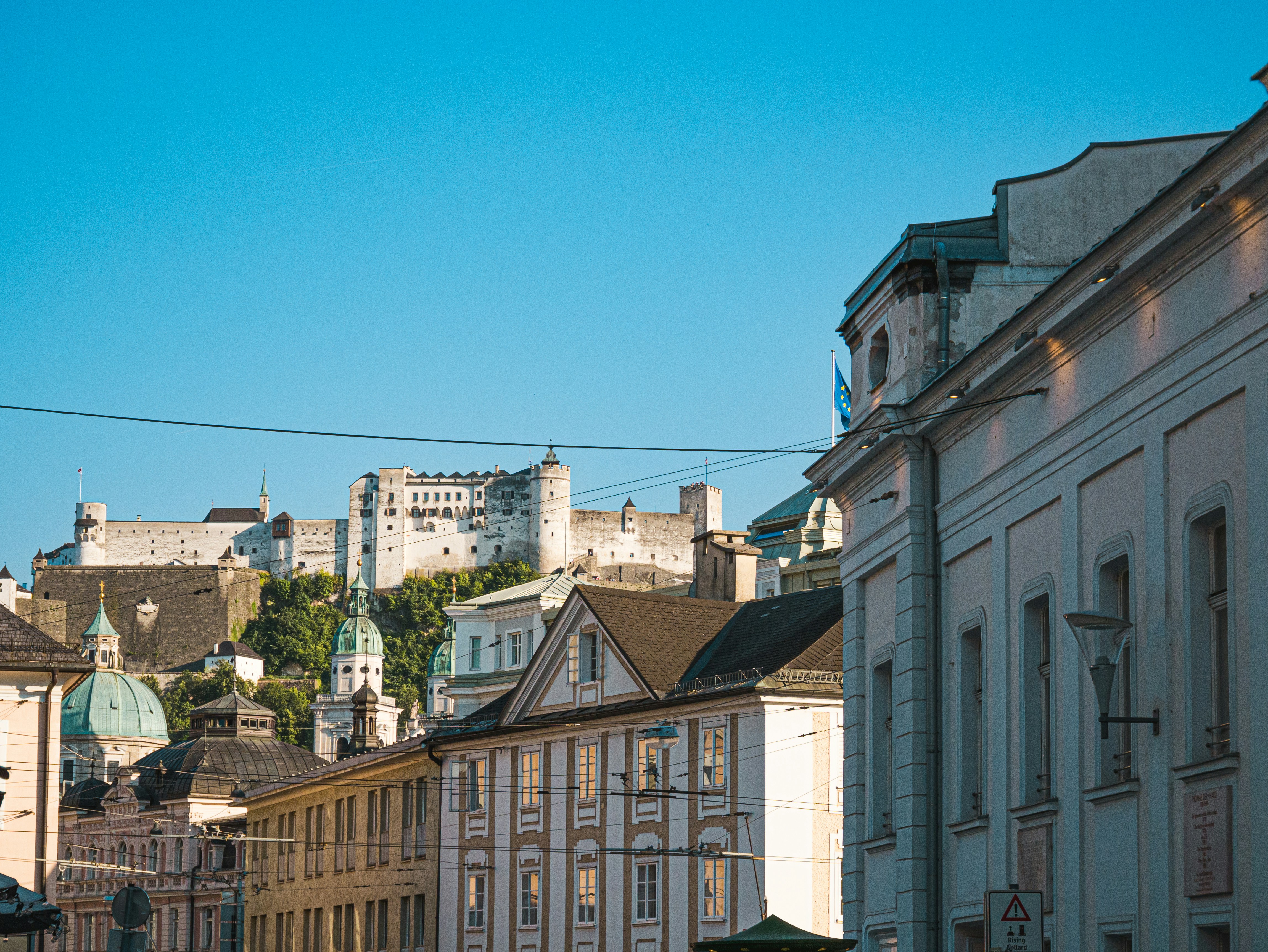 Sunlit Facades and a Castle Across a Quiet European Street