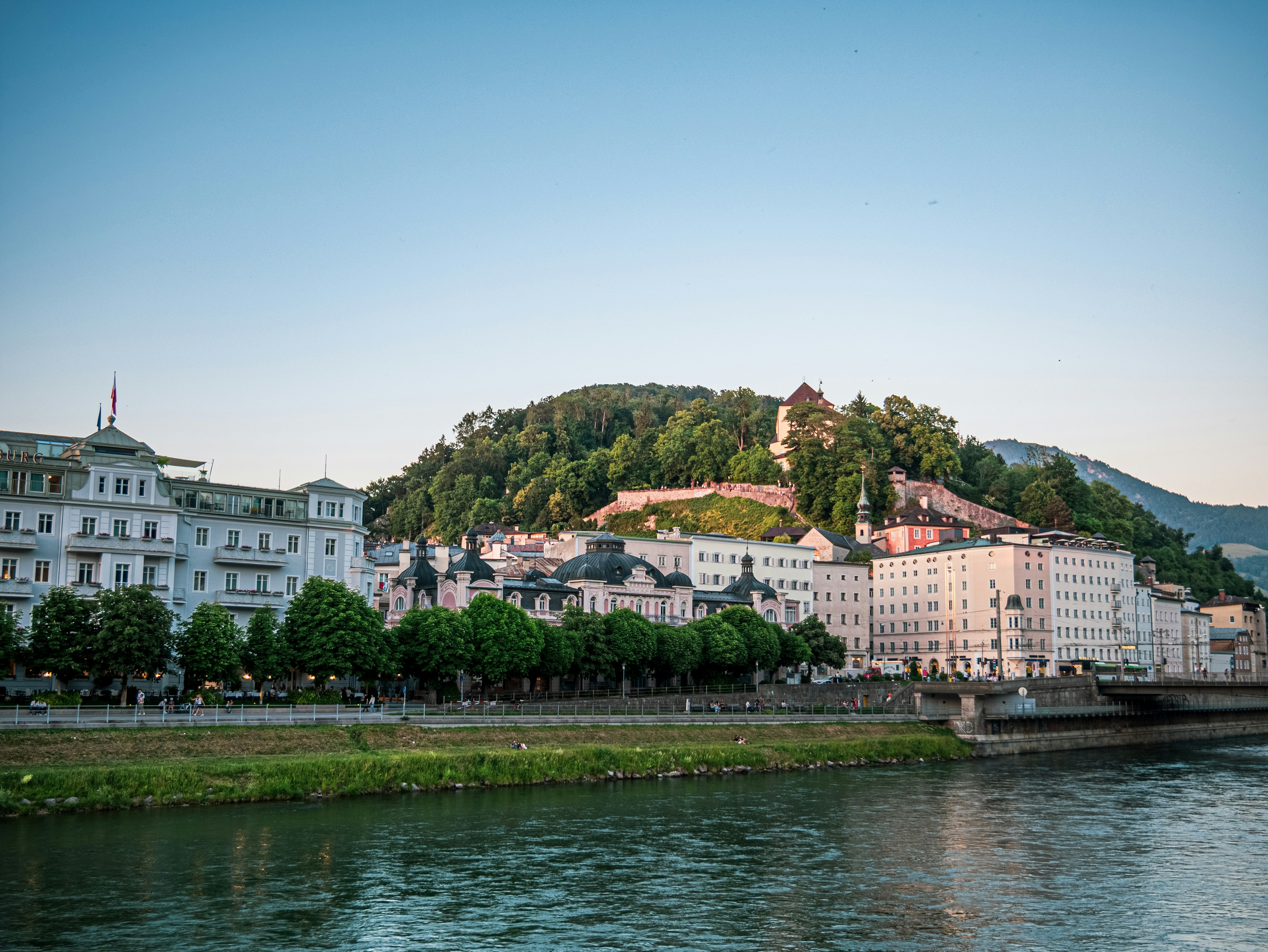 Cityscape with river and castle on a green hill.