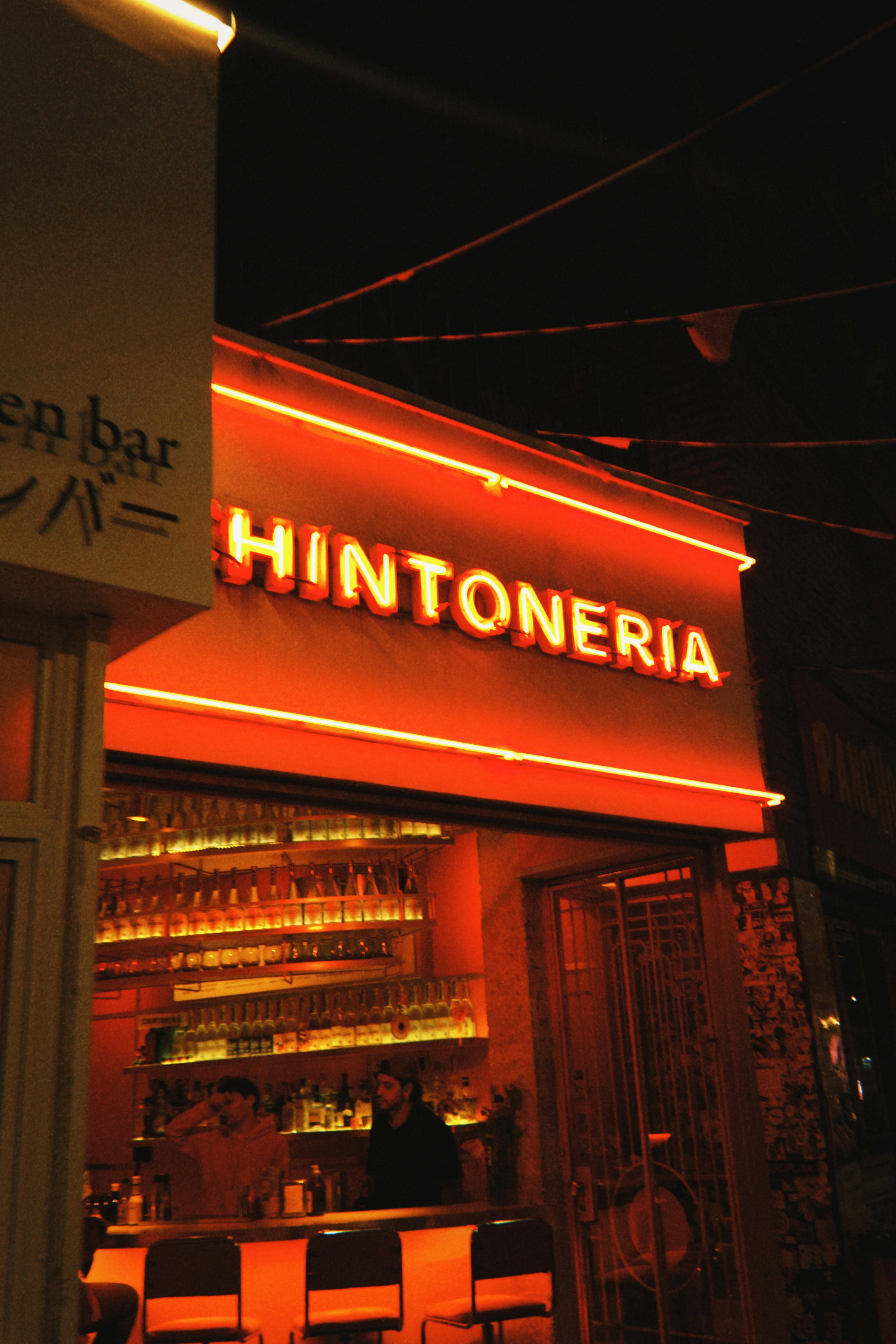 Neon Signage Over a Bustling Barfront at Night