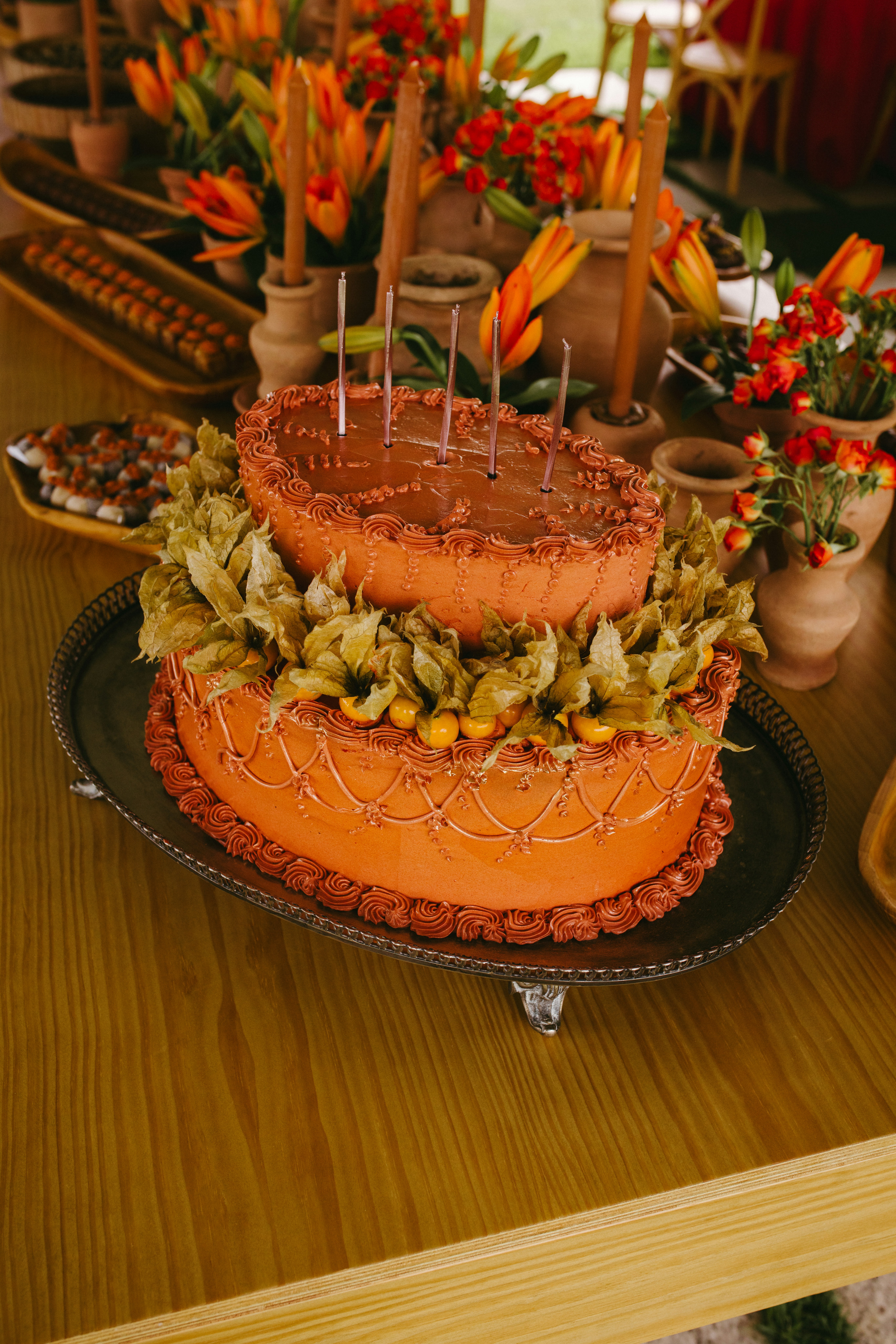 Two-tiered orange cake with physalis decorations on a wooden table.