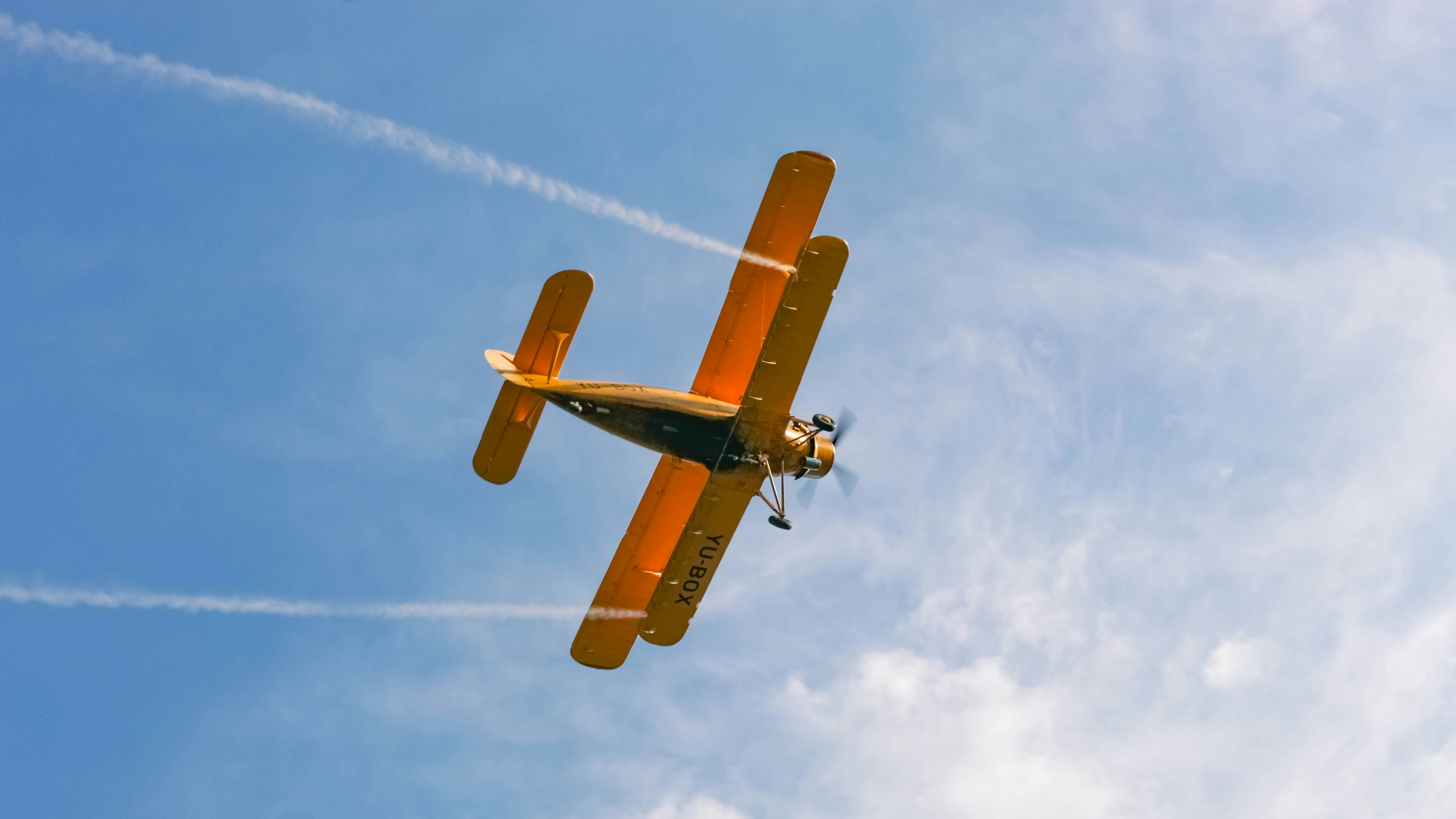 Yellow biplane flying in blue sky with white contrails.