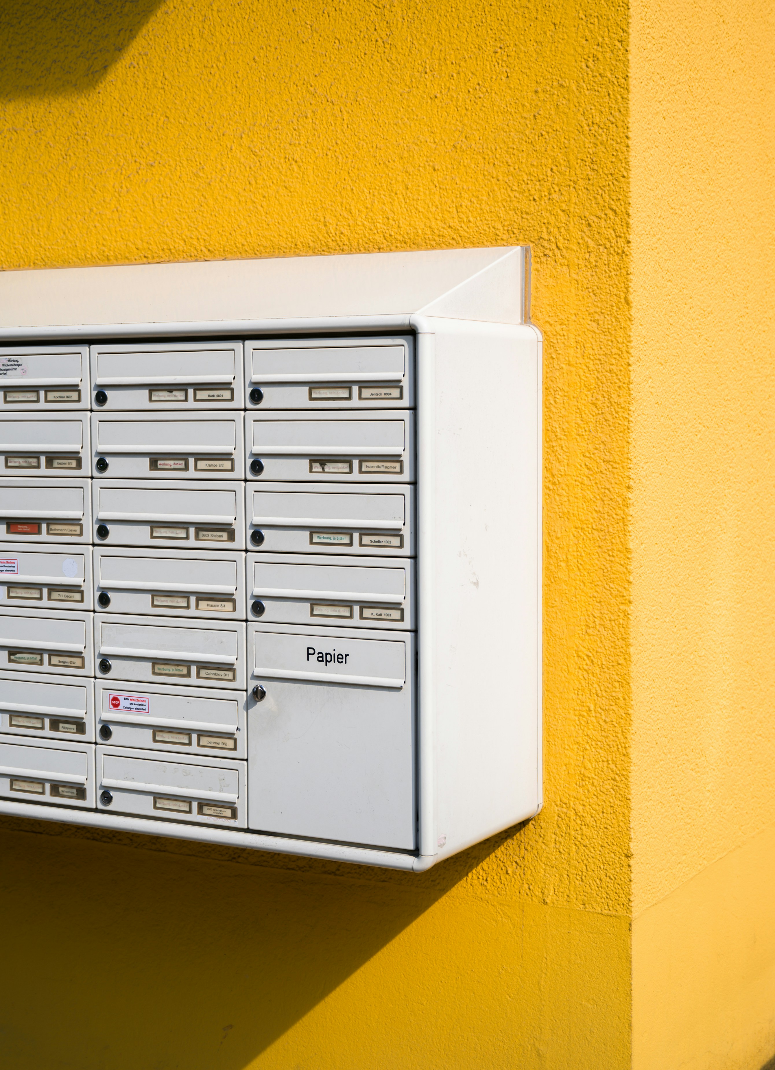 Yellow Post: A Row of Mailboxes Dimly Cast Against a Bright Facade