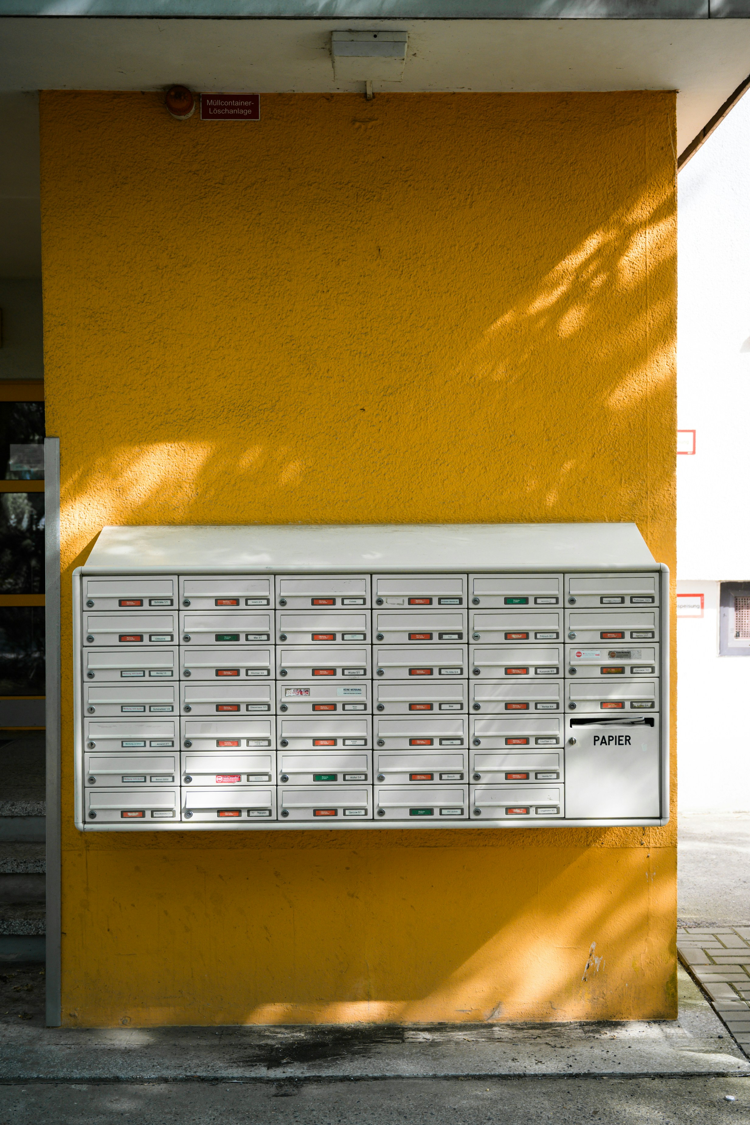 Multiple white mailboxes on a bright yellow wall.