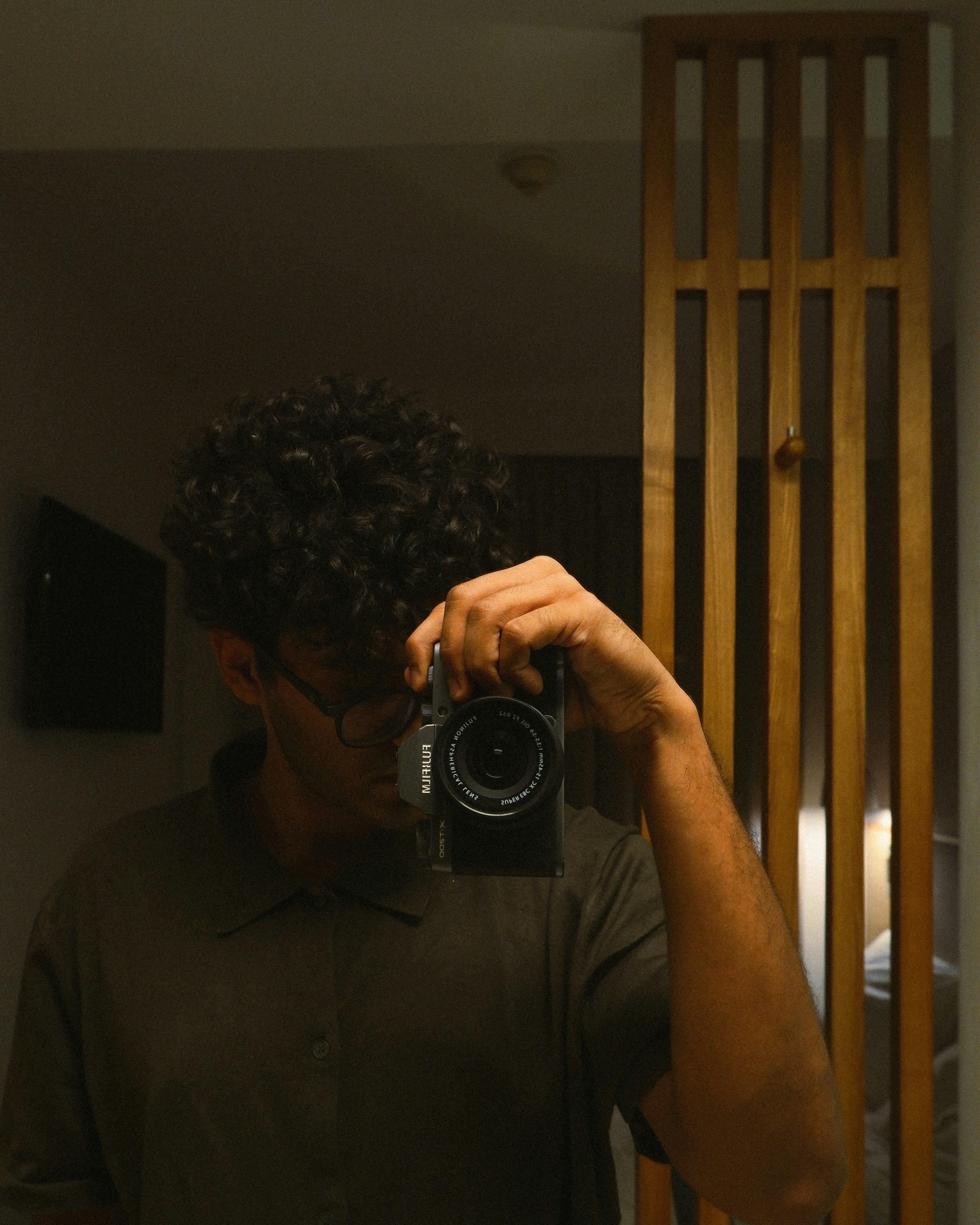 Man with curly hair taking mirror selfie with camera.