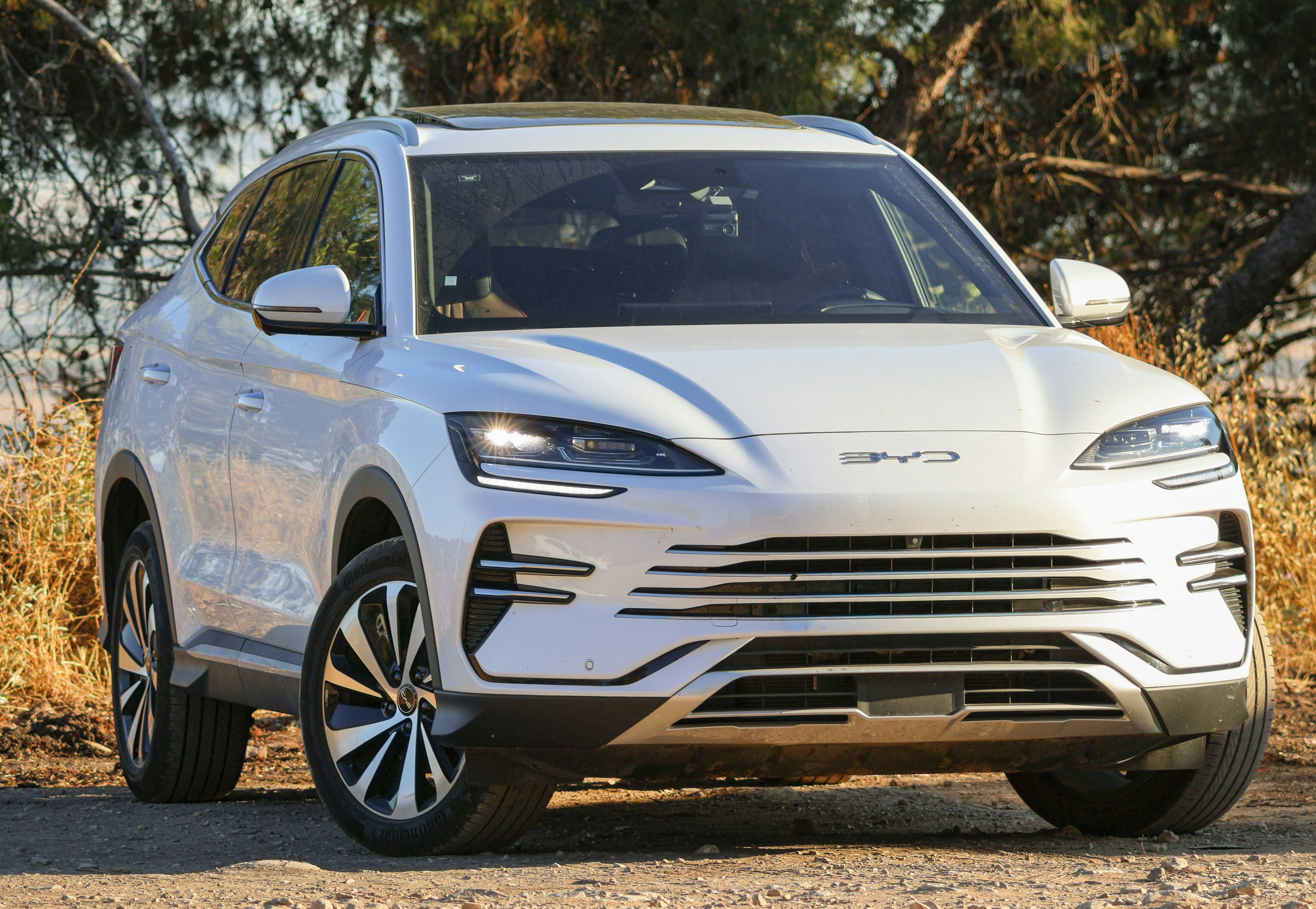 A white electric suv parked outdoors on a dirt road.