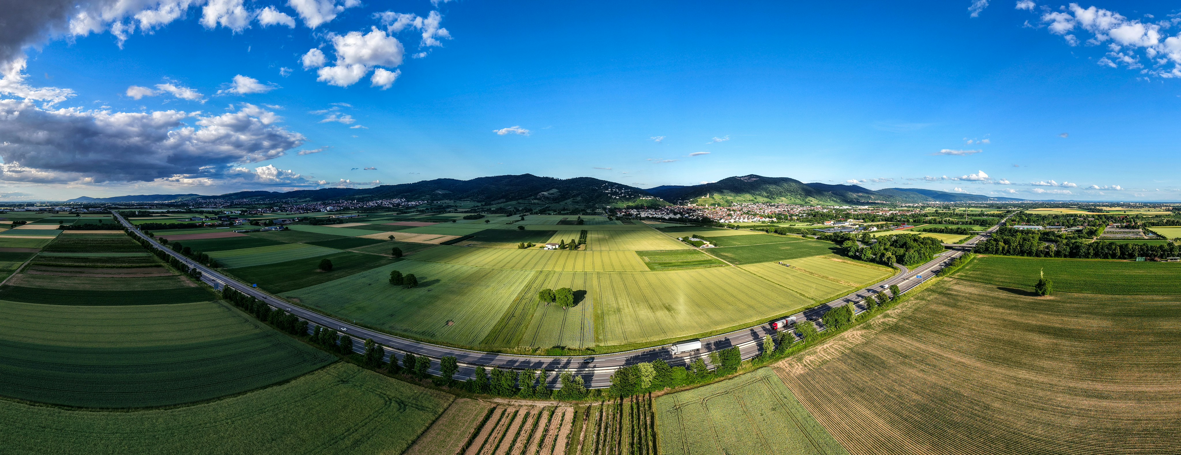 Panoramic rural landscape with a curved road and green fields.