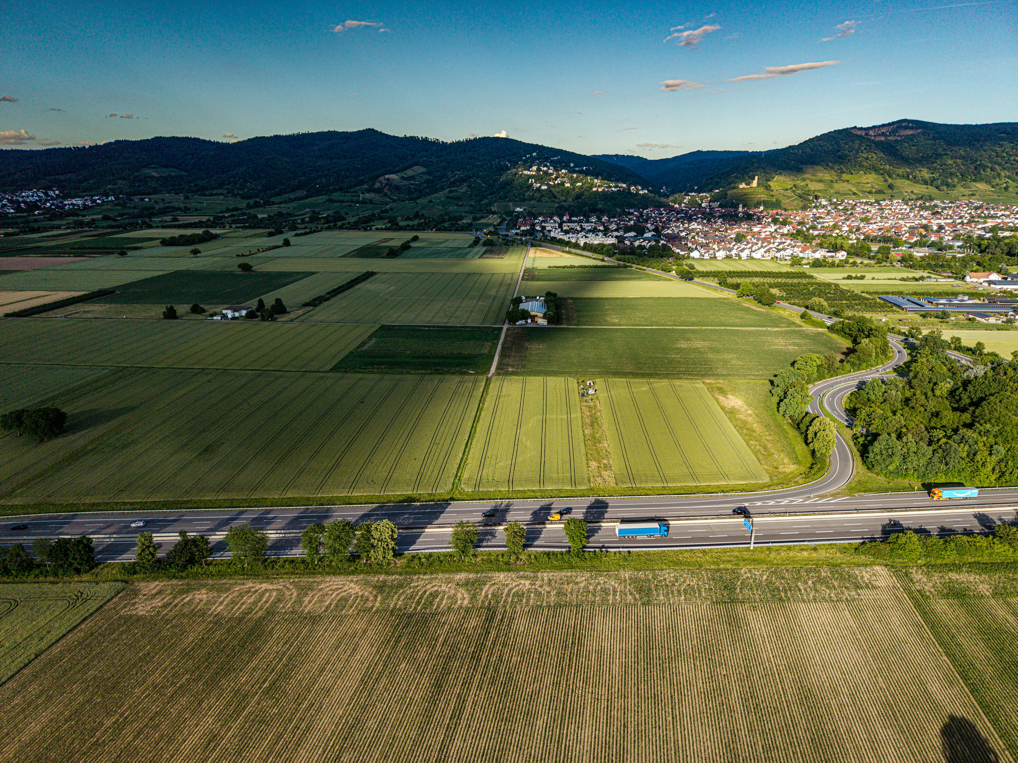 Sunlight and shadows on fields, highway, and distant mountains.