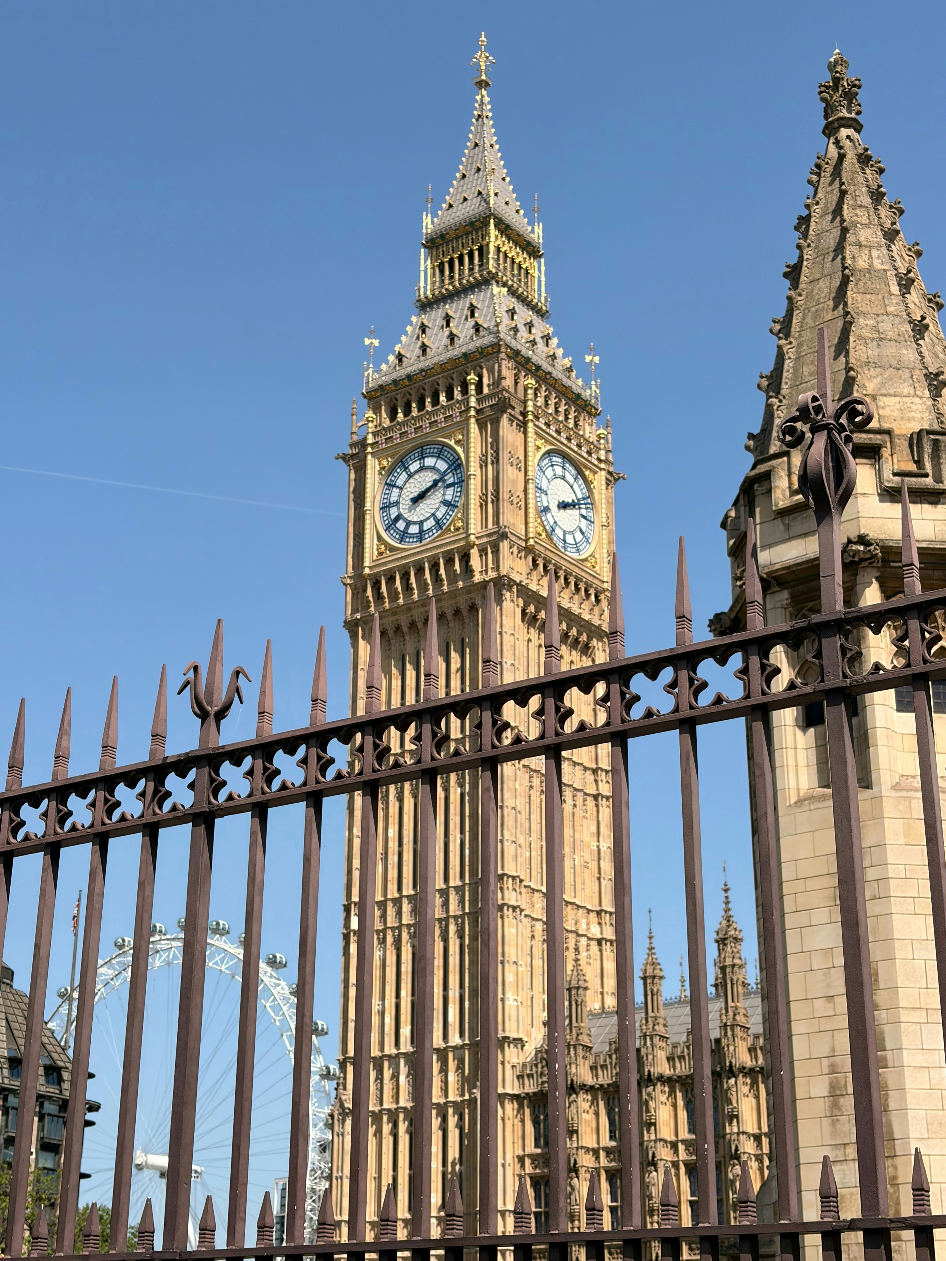 Clock Tower and Gothic Spires Framed by Urban Fence