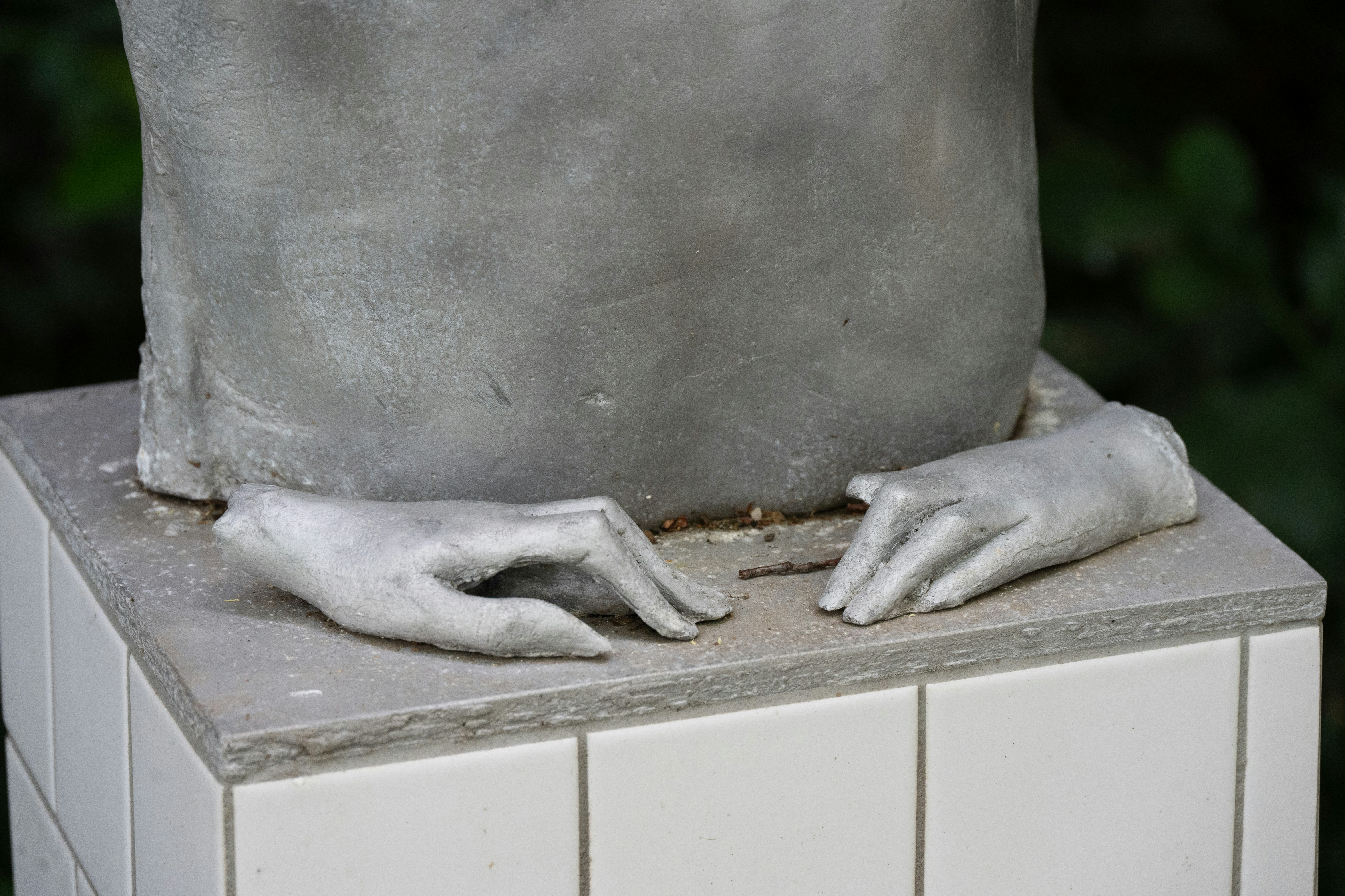 Grey statue torso and detached hands on a tiled pedestal.