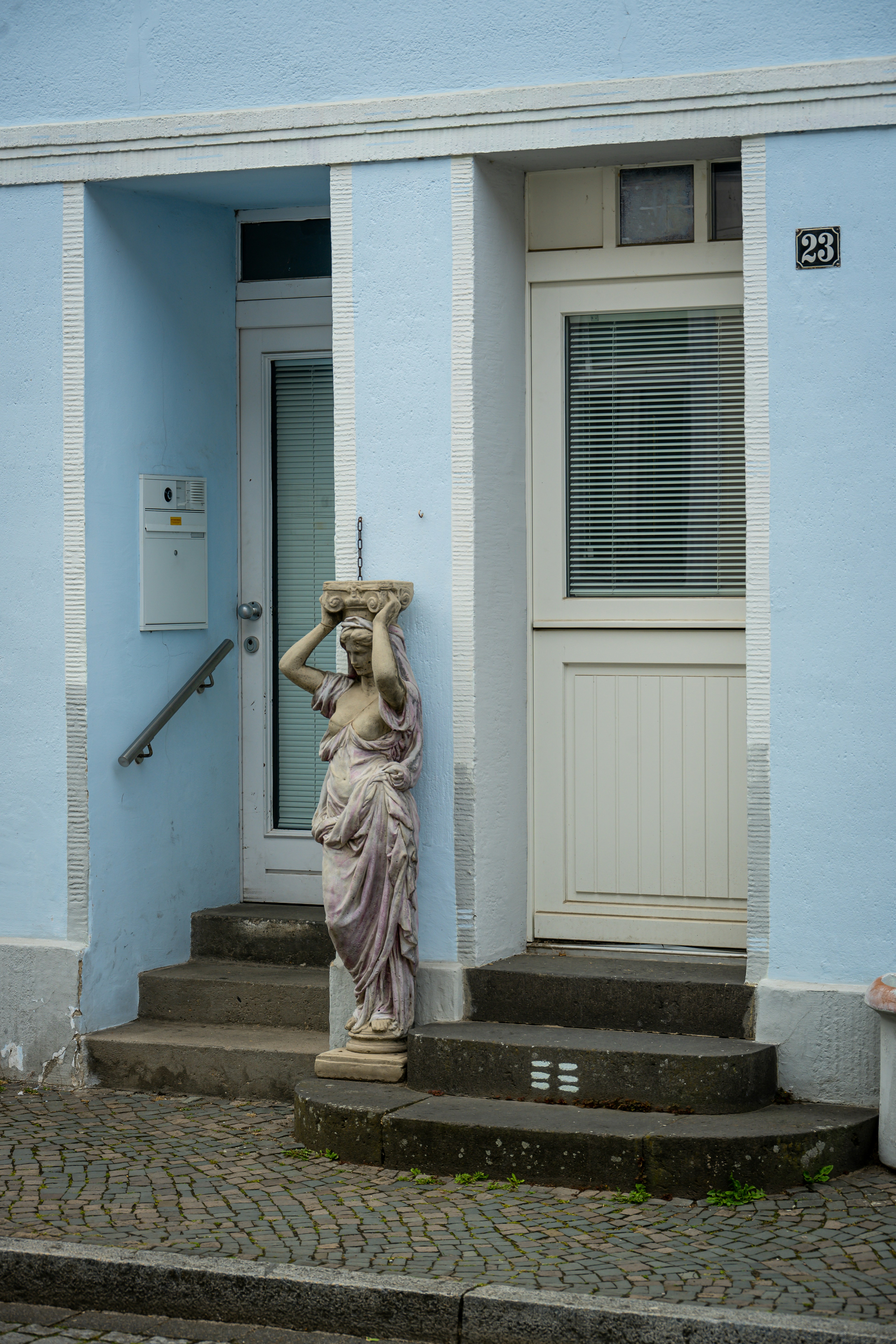 Statue at the Blue Doorway: Classical Graces Meet Modern Facade