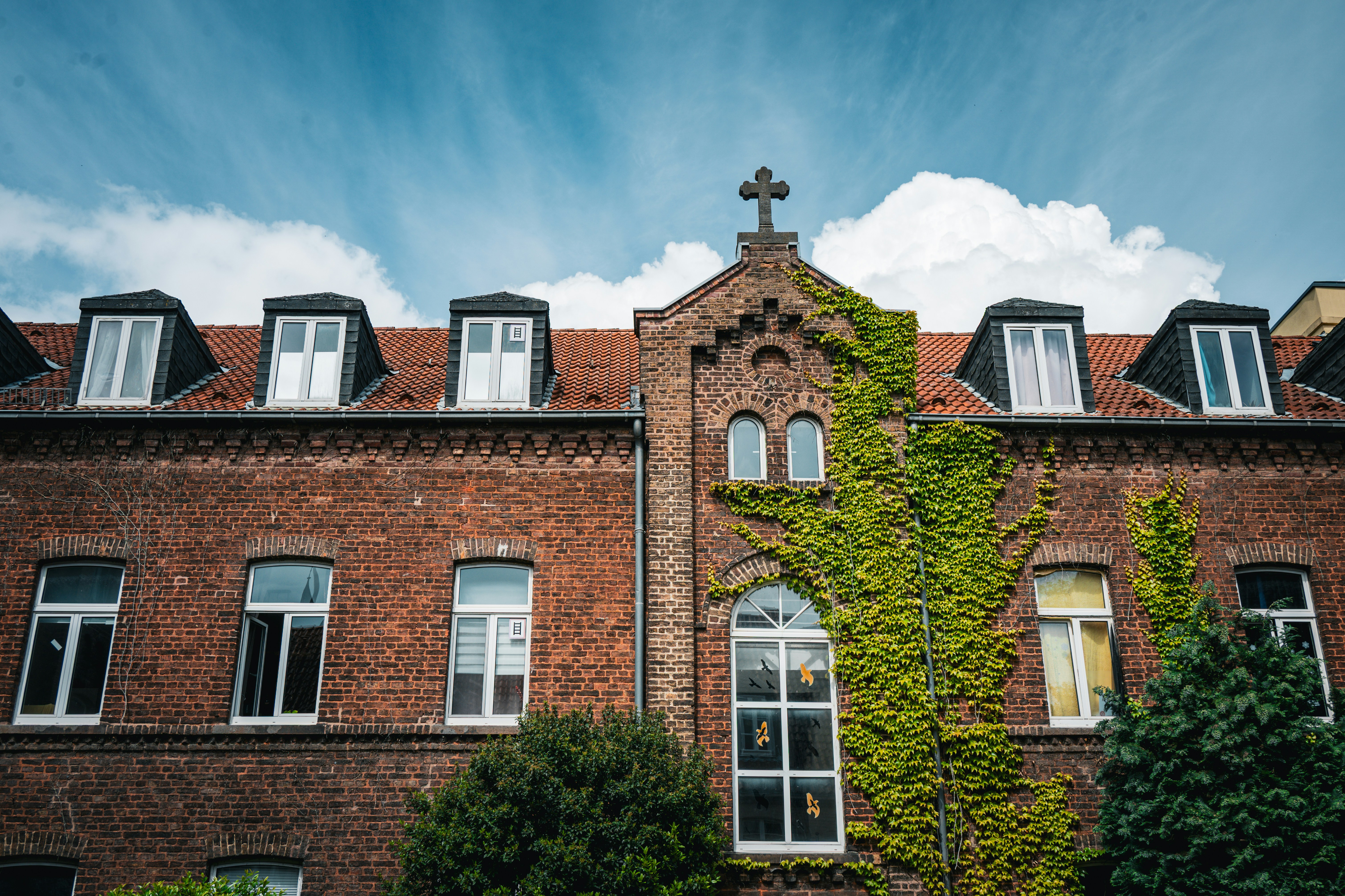 Historic brick building with green ivy and a cross.