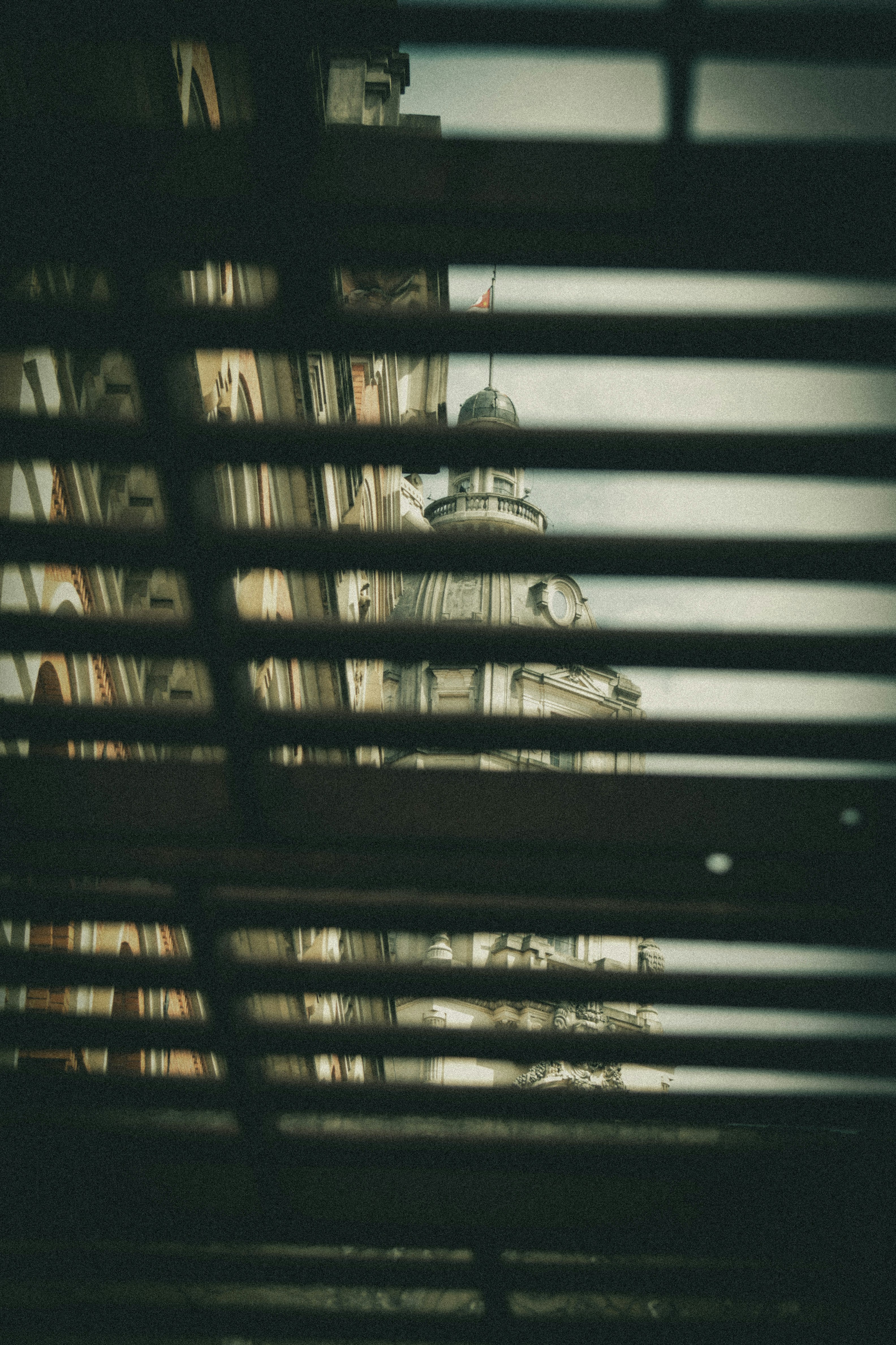 Through Narrow Slats: A Clock Tower Emerges Between Shadows