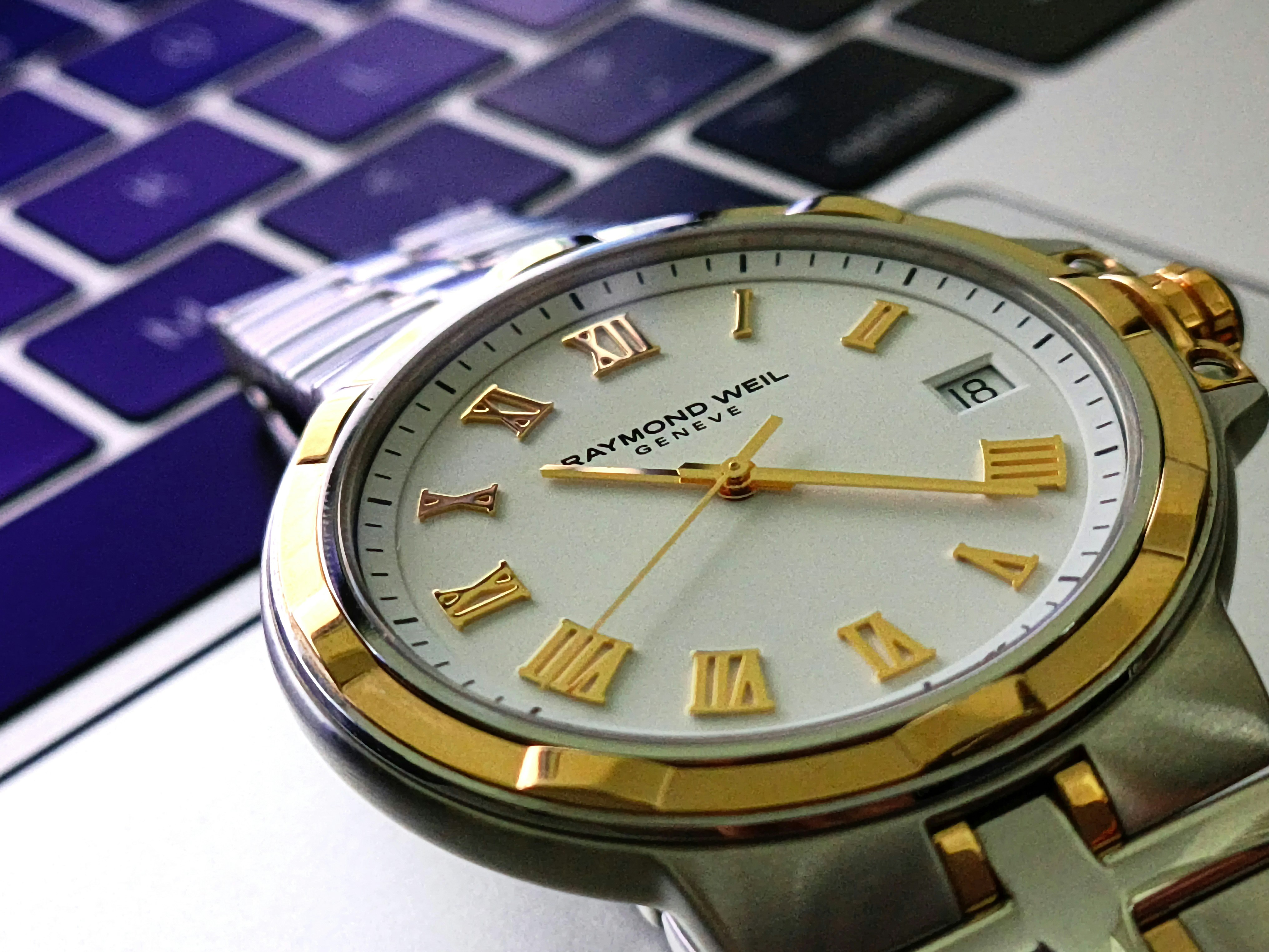 Close-up shot of a classic two-tone Raymond Weil Parsifal men's dress watch featuring a white dial, gold Roman numeral markers.