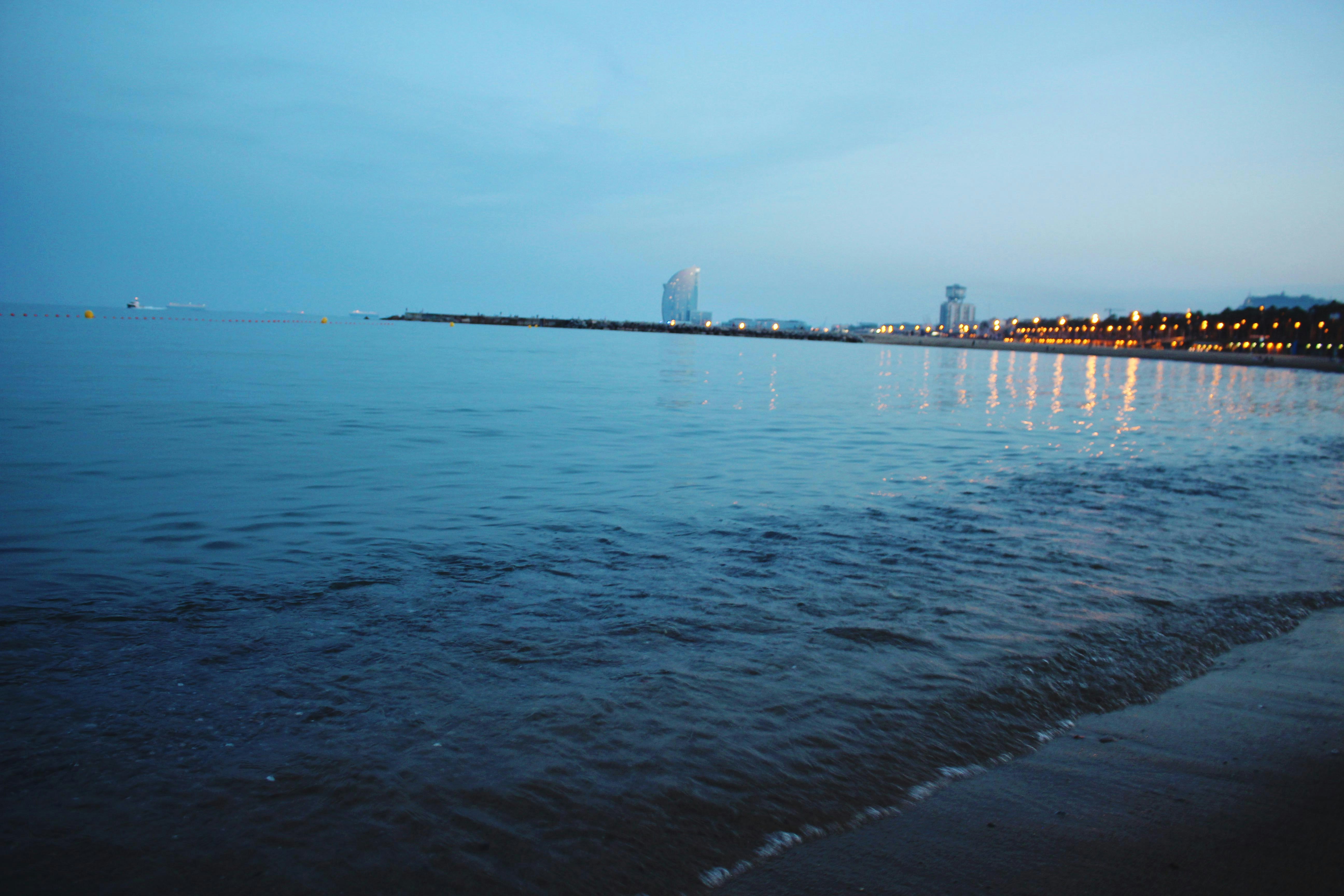 Dawn on a Quiet Seaside: City Lights Reflecting on Calm Waters