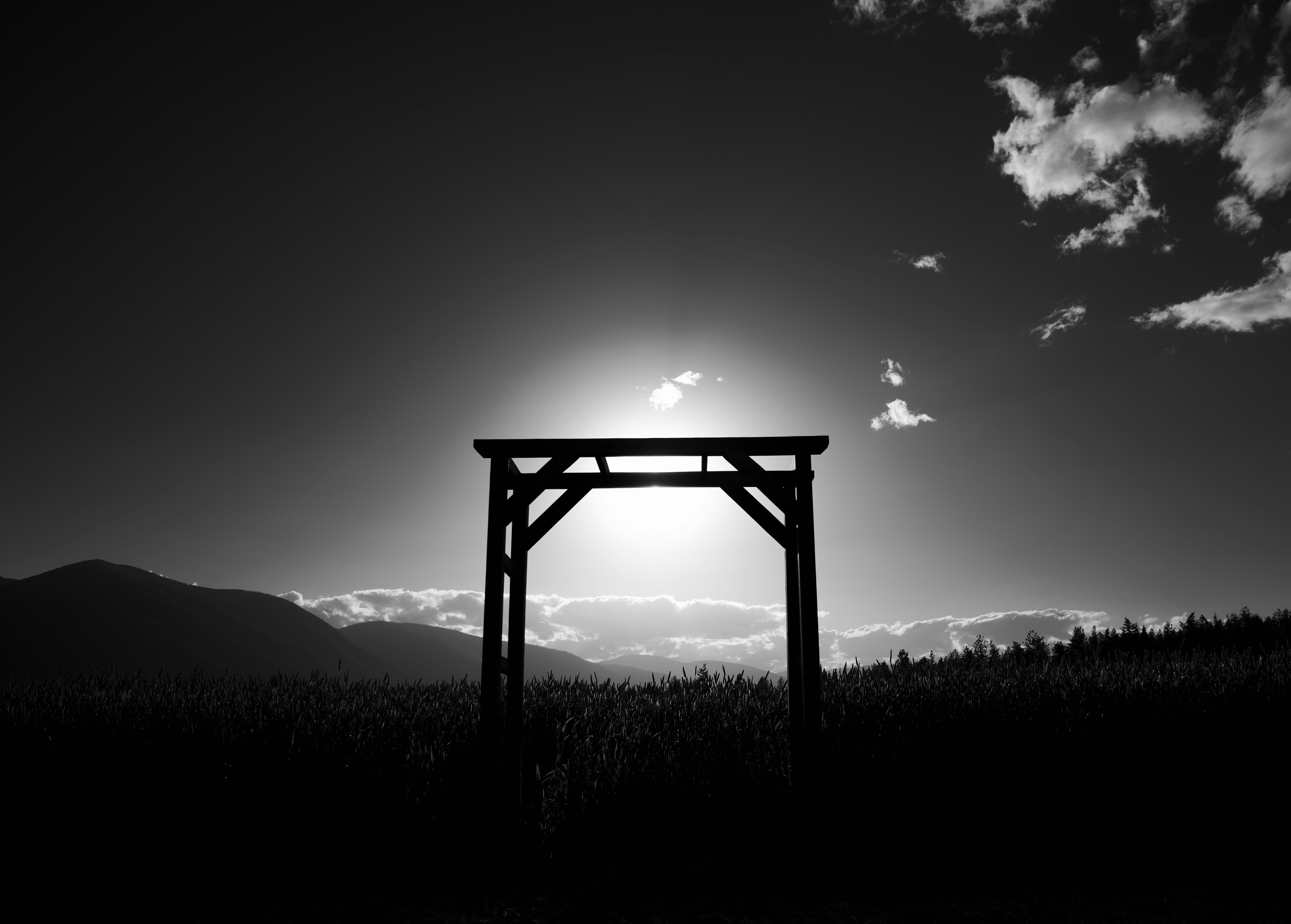 Silhouetted wooden archway against bright sun and mountains.