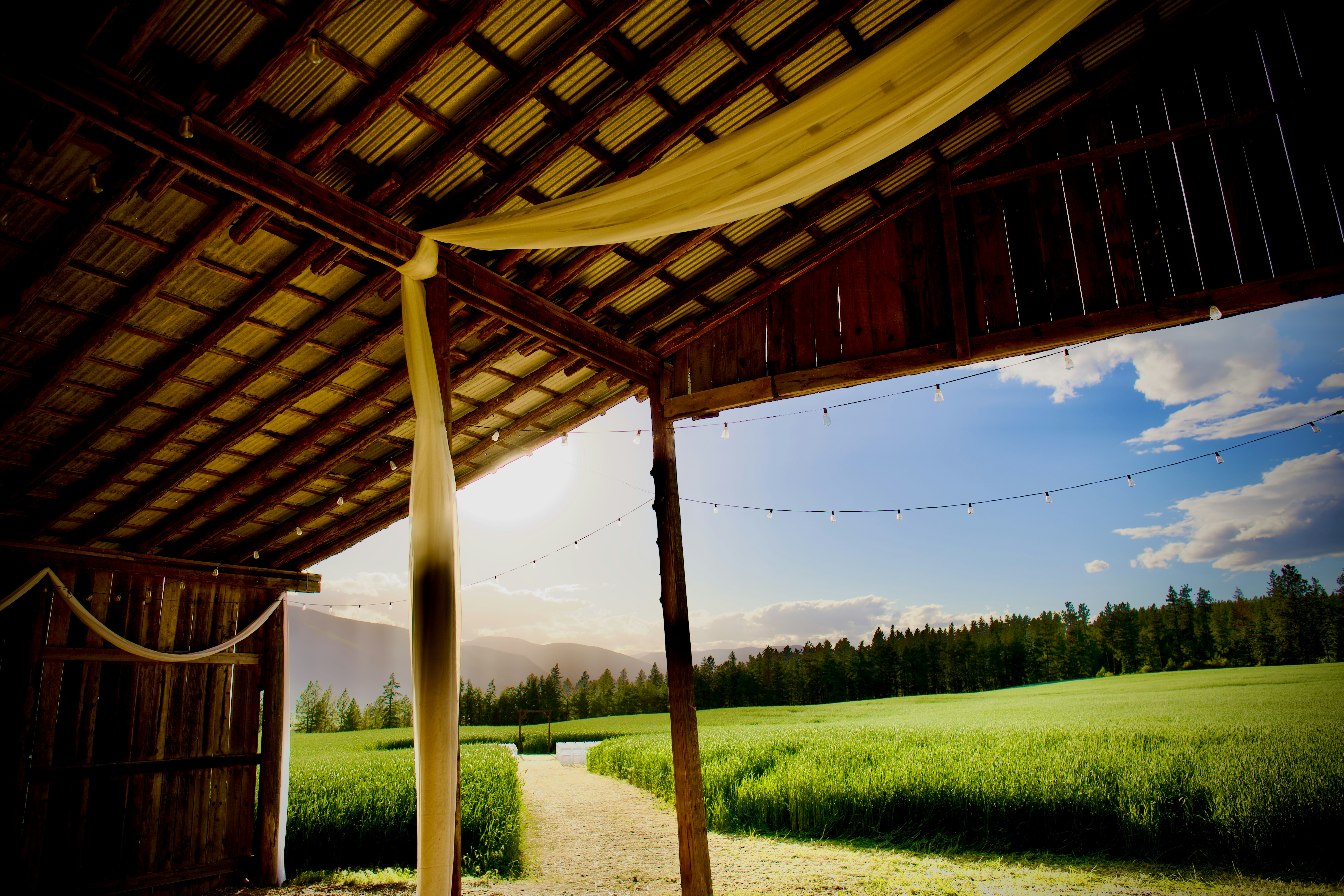 Rustic barn interior frames a vibrant green field and mountains.