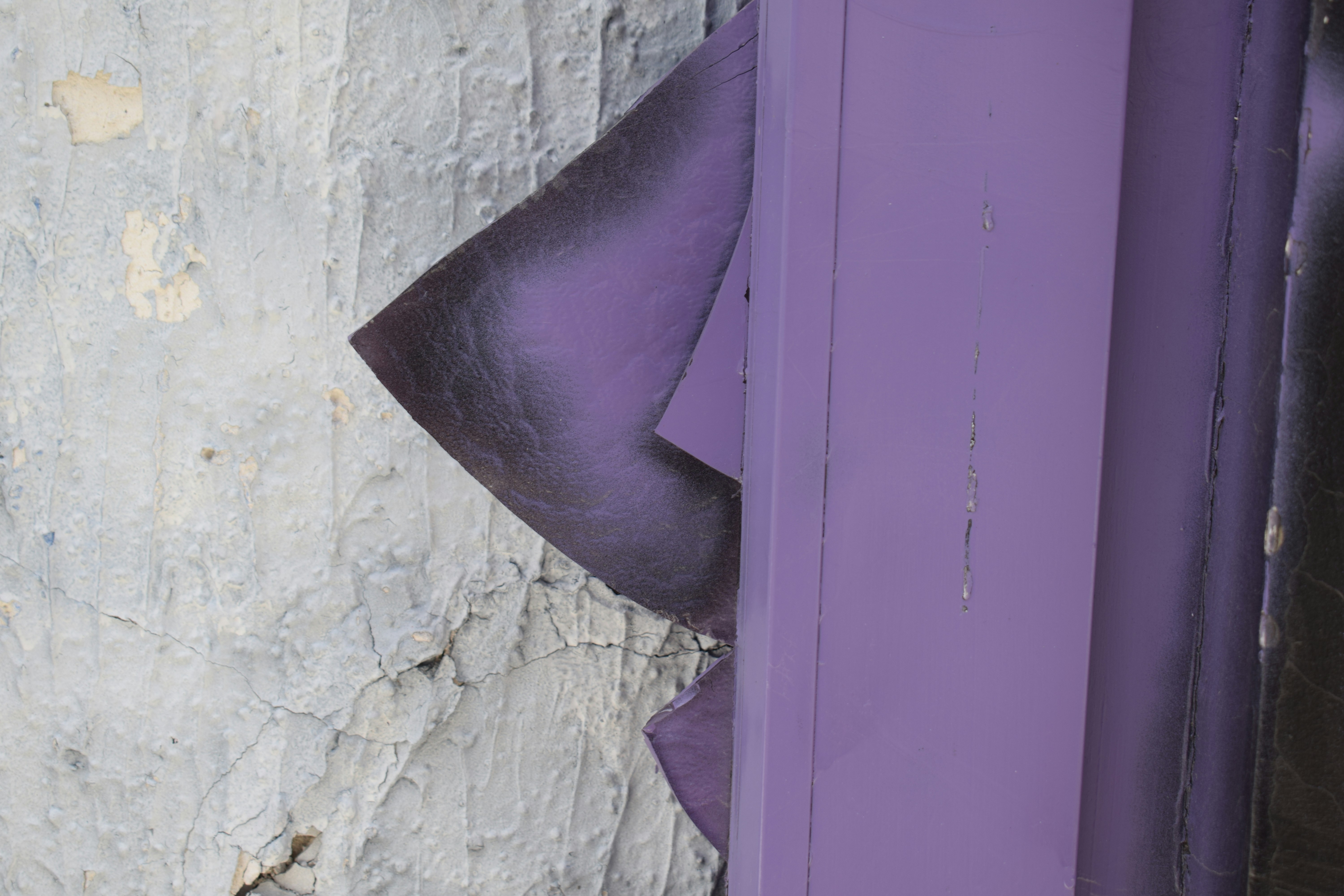 Purple Metal Fold: A Striking Sliver of Color Against Weathered Concrete
