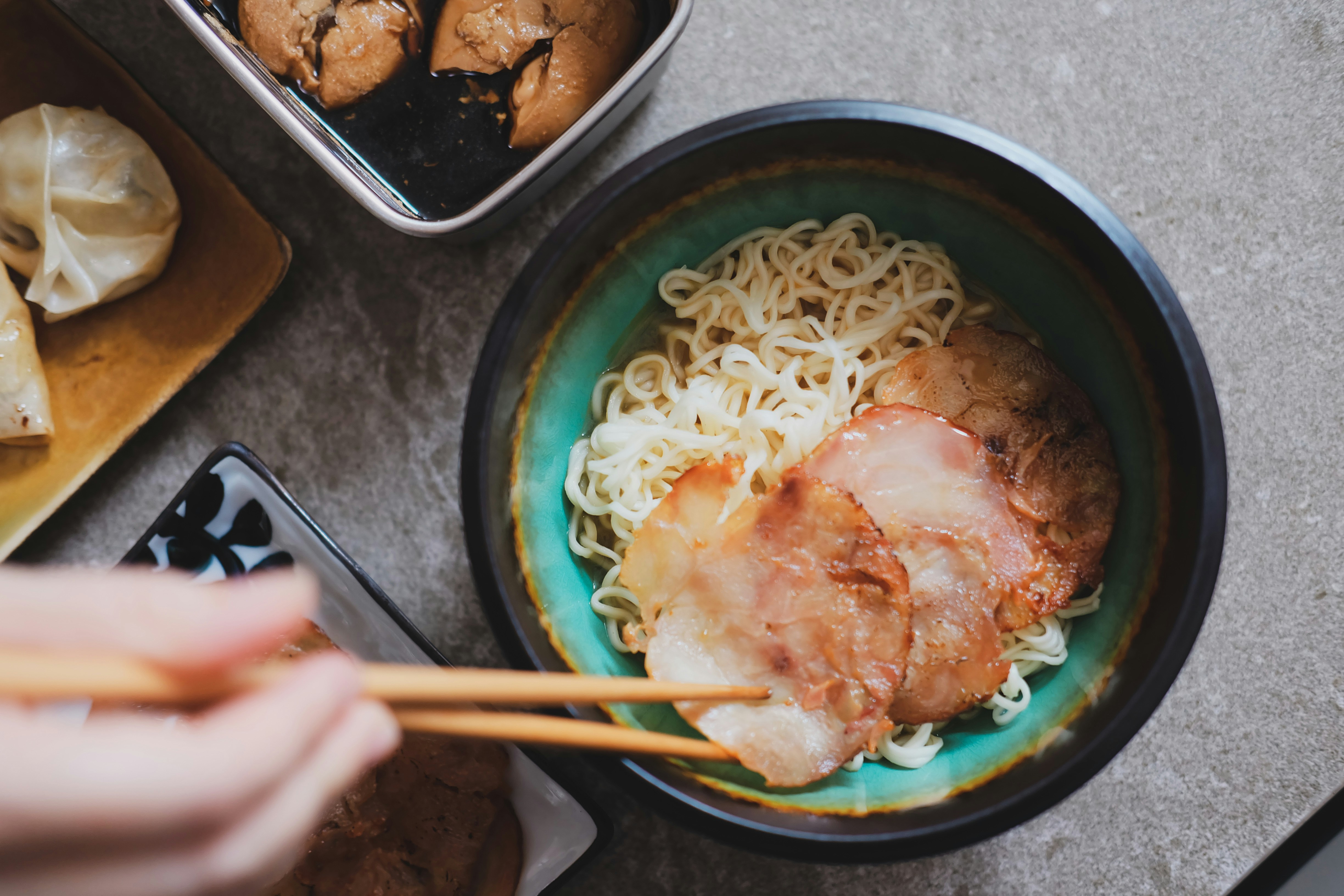 Hand using chopsticks to eat noodles with pork.