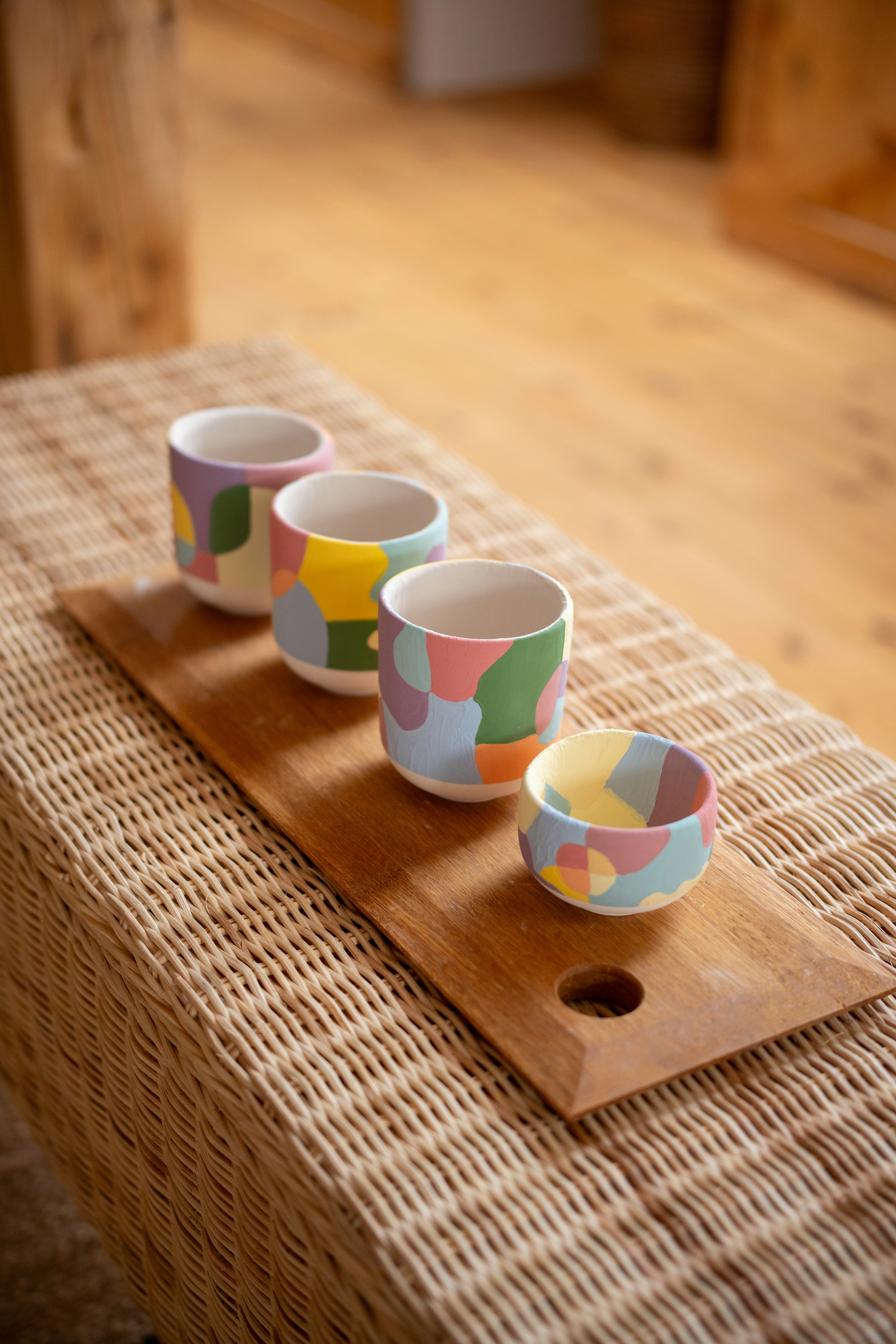 Colorful abstract ceramic cups on a wooden board.