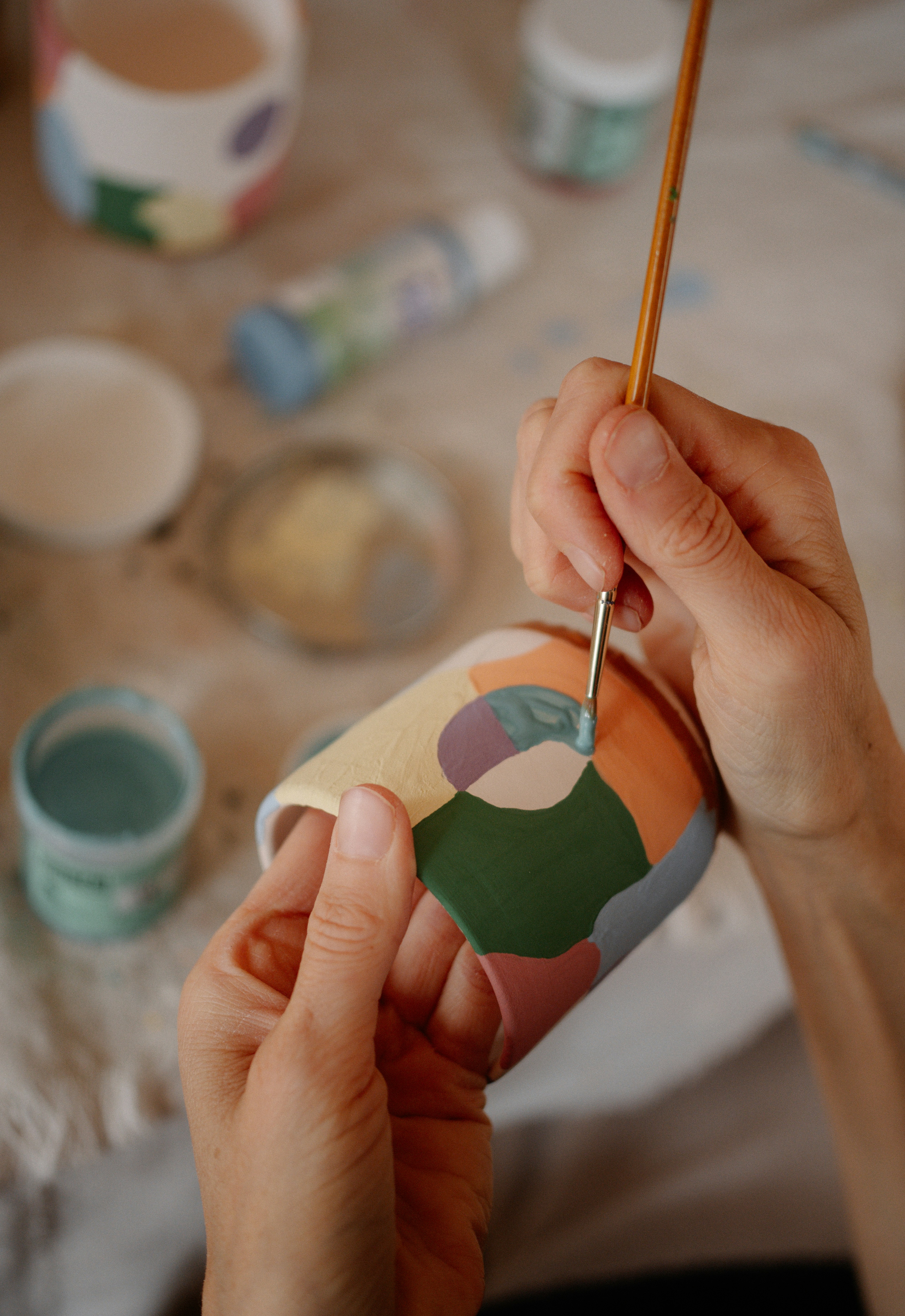 Hands painting abstract designs on a ceramic cup.