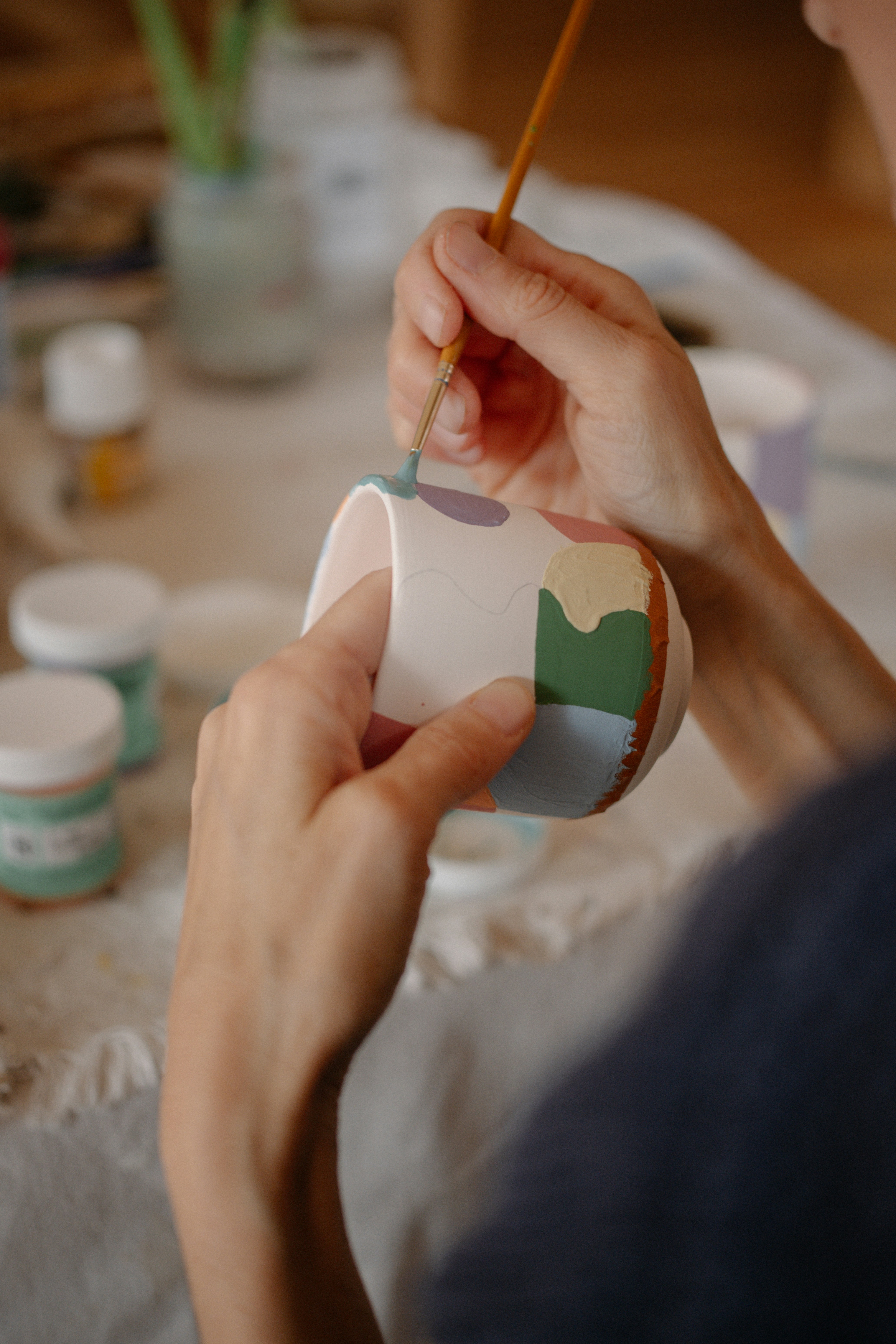 Hands painting colorful abstract designs on a ceramic mug.