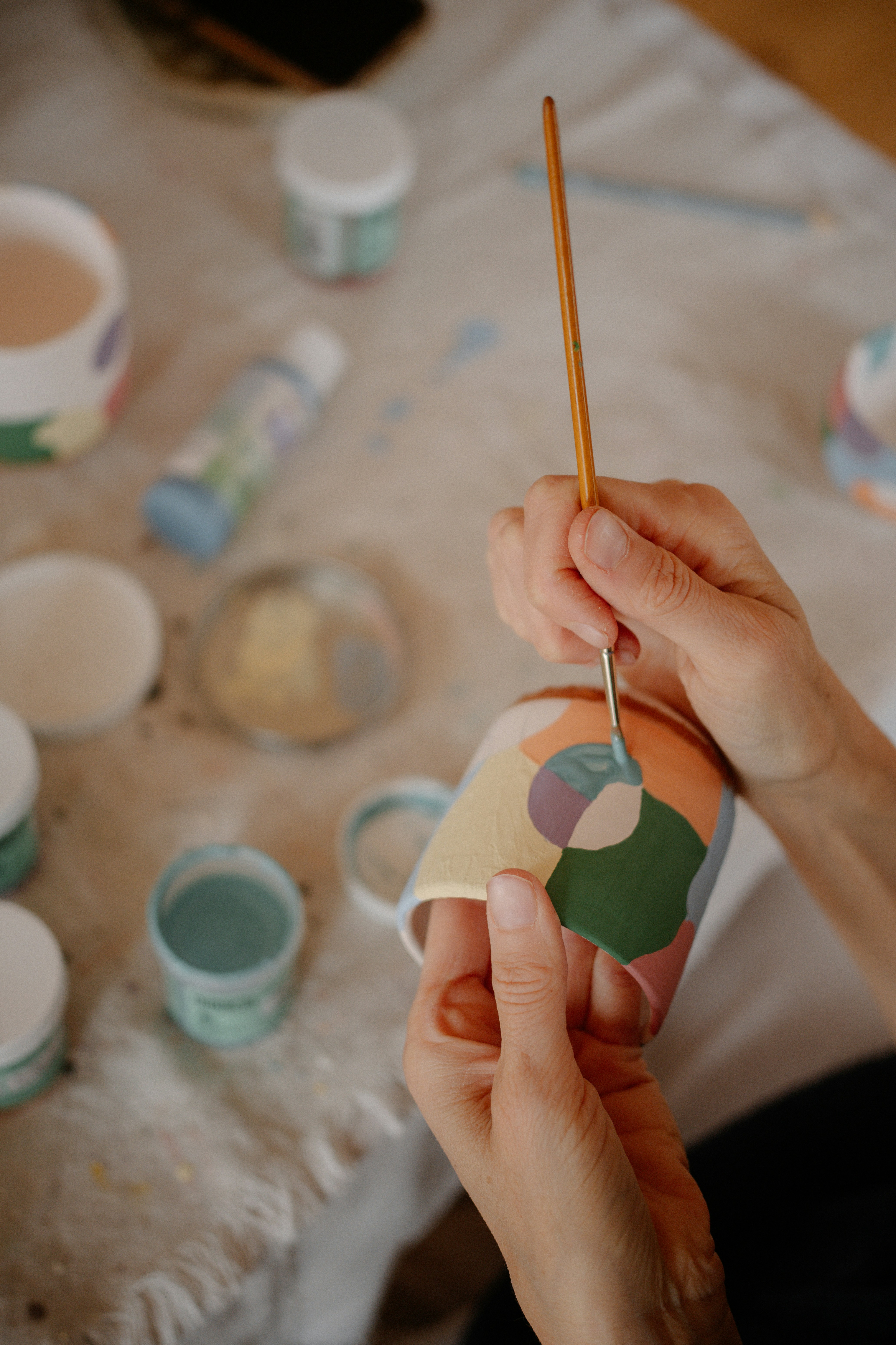 Hands painting a ceramic mug with colorful designs.
