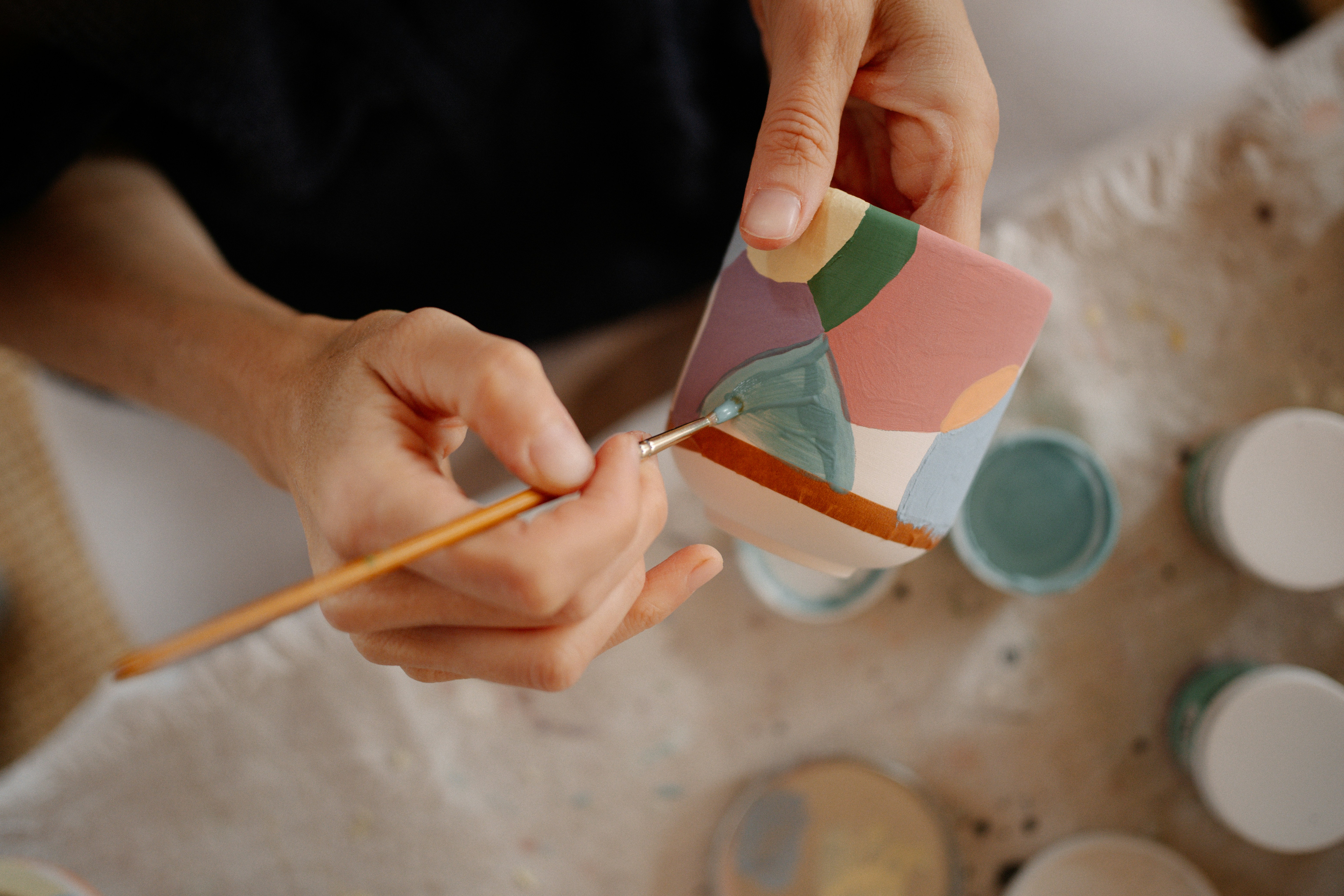 Artist's hands painting a colorful ceramic piece.