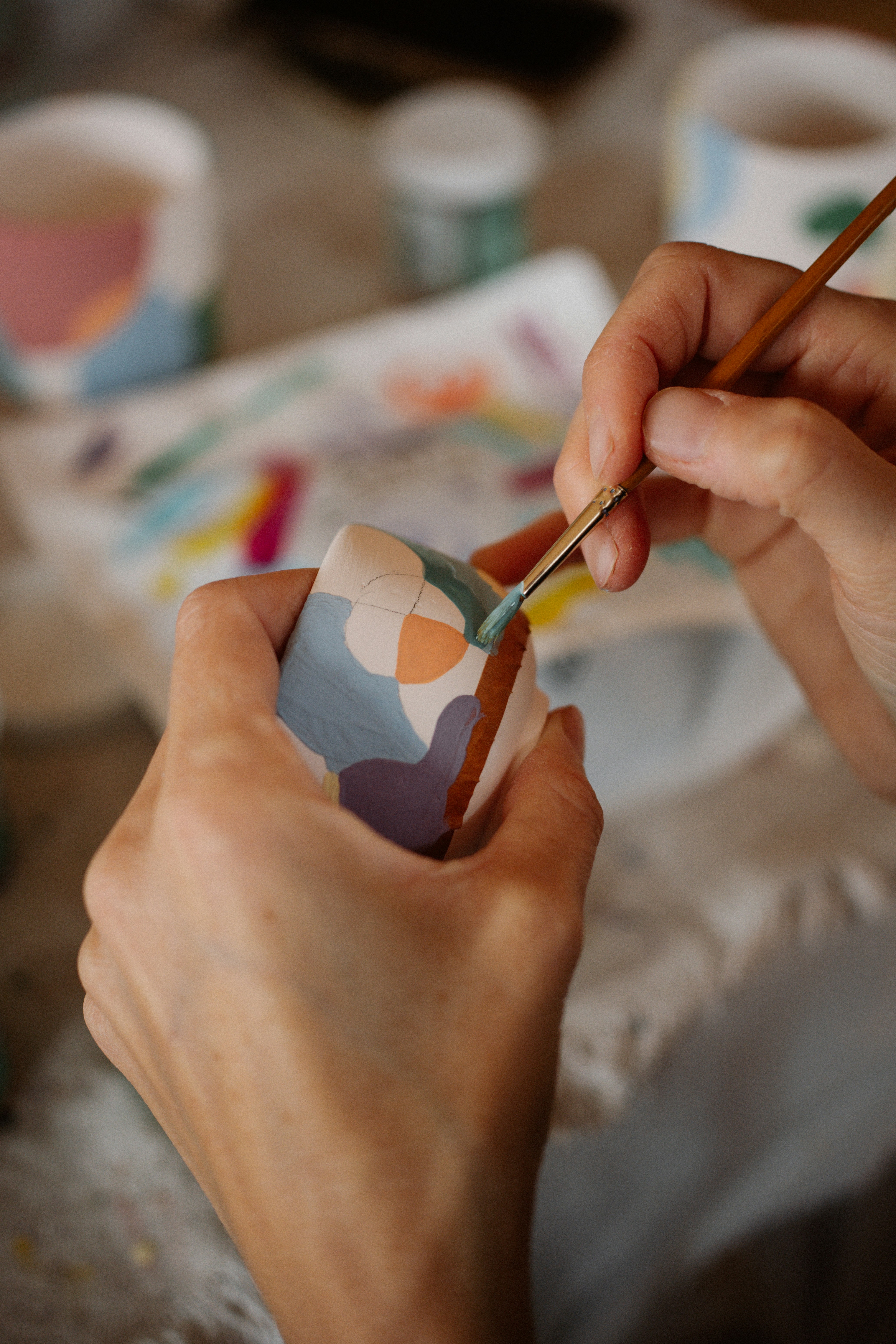 Hands painting colorful abstract patterns on a small ceramic piece.