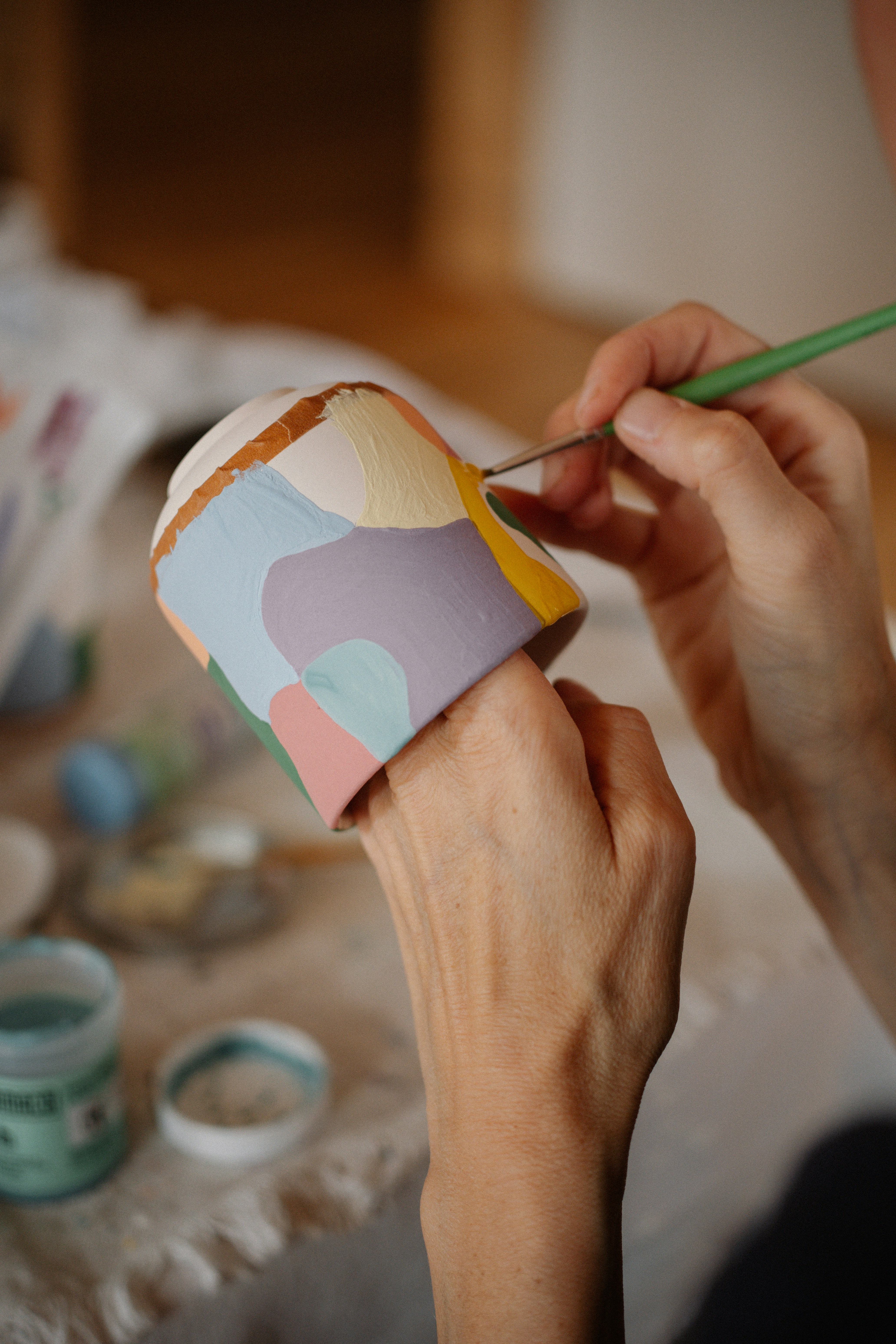 Hands painting colorful abstract patterns on a ceramic cup.