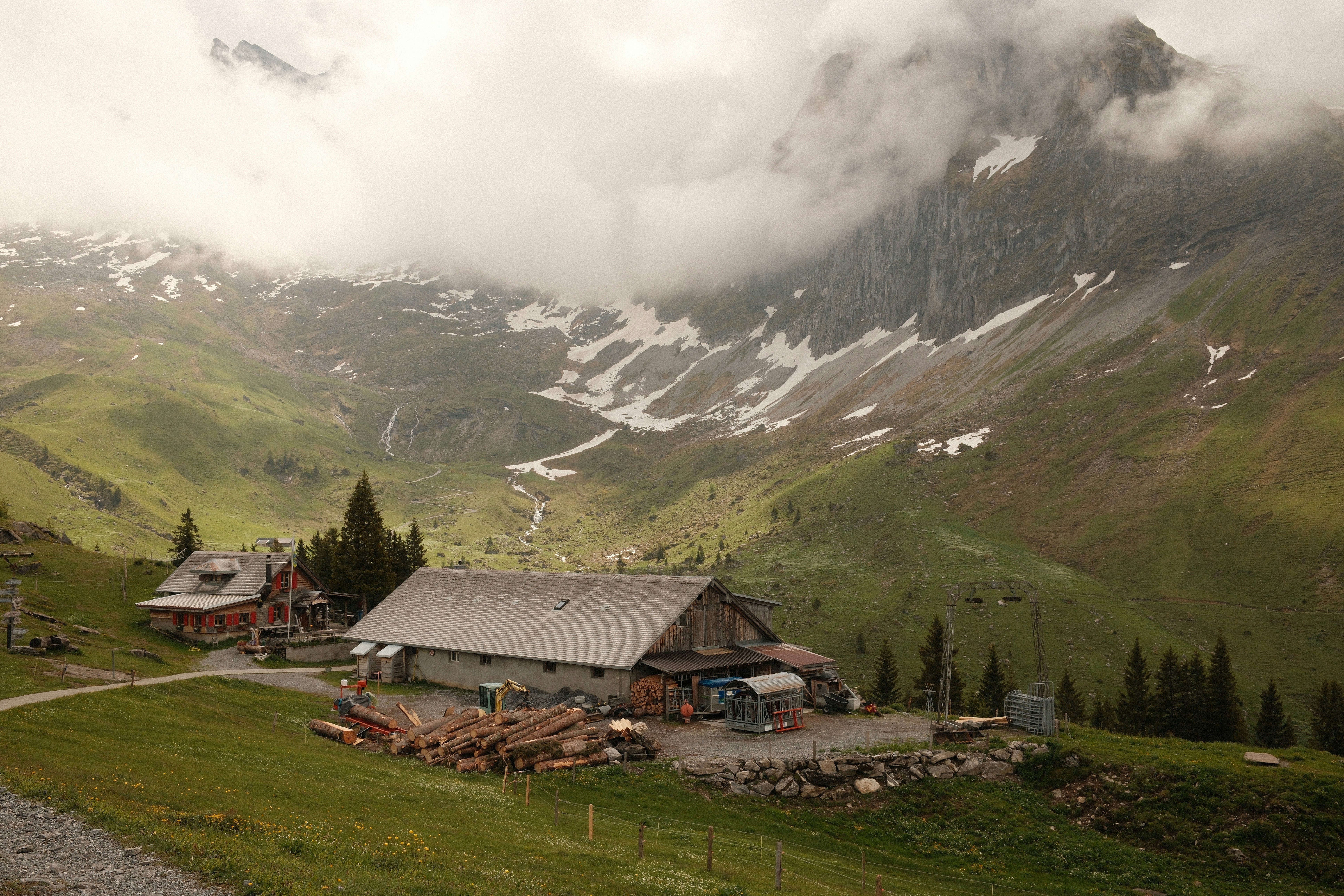 Mountain valley with traditional buildings, green slopes, and cloudy peaks.