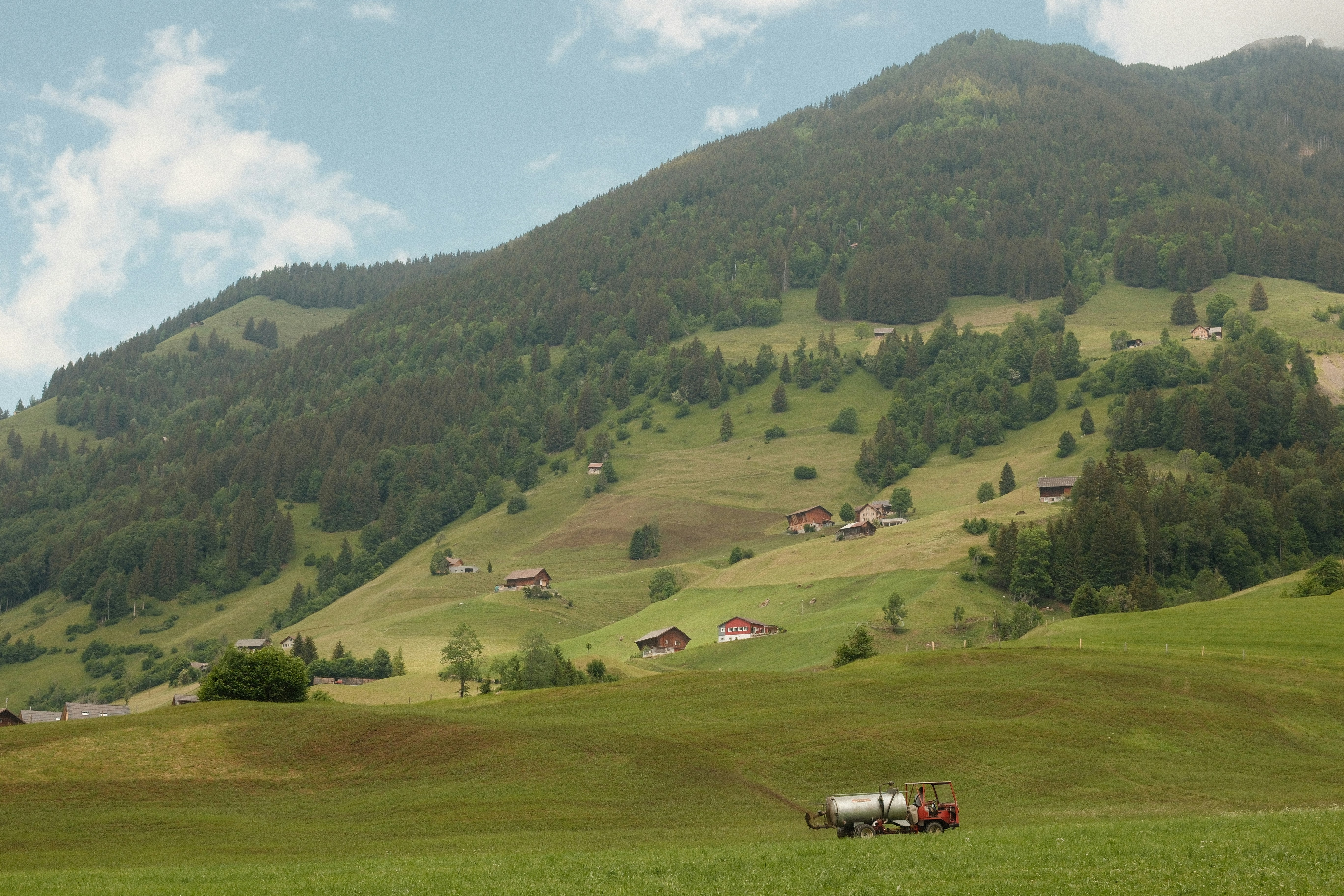 Tractor working in a green field near a forested mountain.