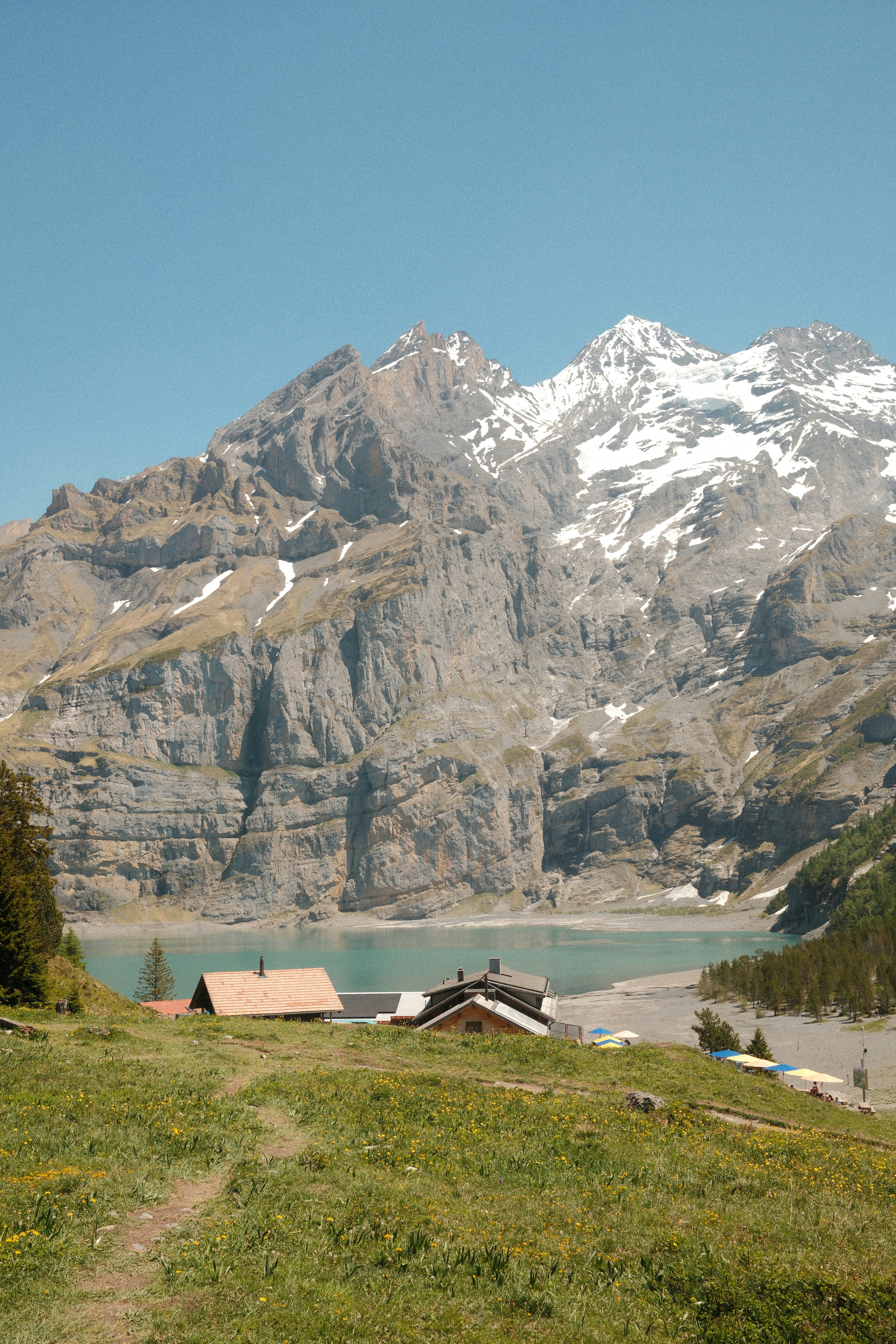 Houses by a turquoise lake with snow-capped mountains in background.
