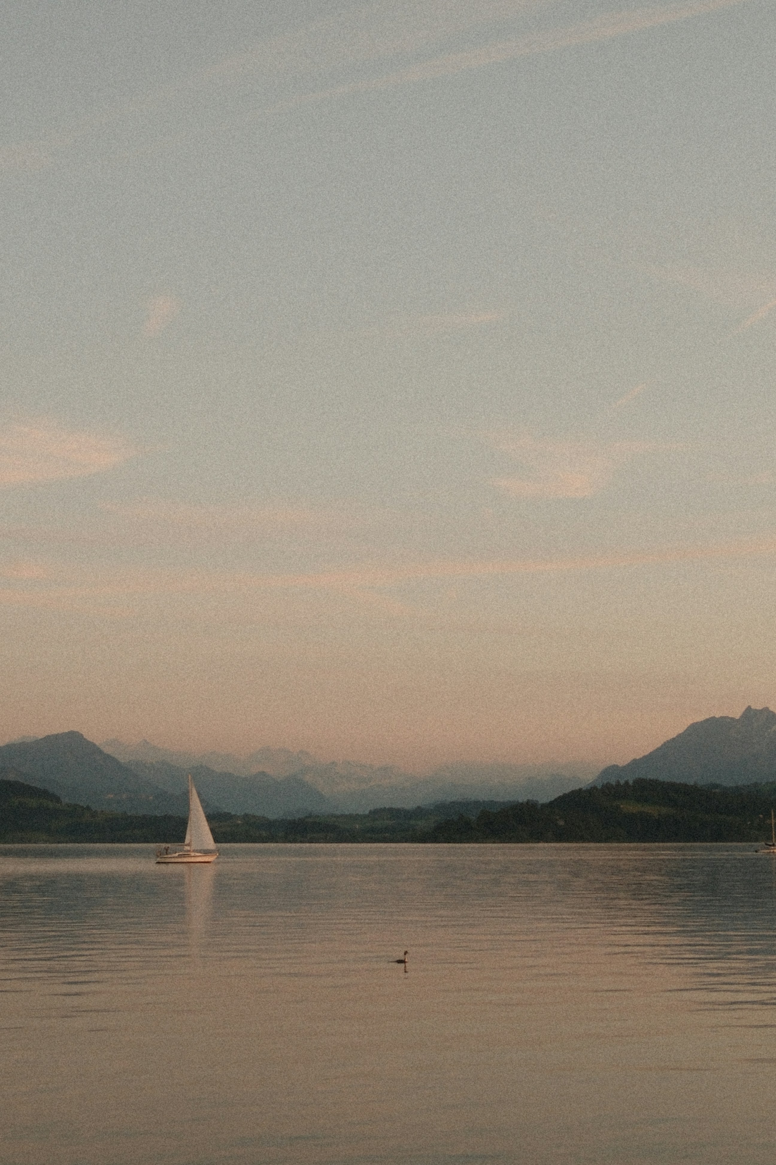 Sailboat on a calm lake with distant mountains at sunset.
