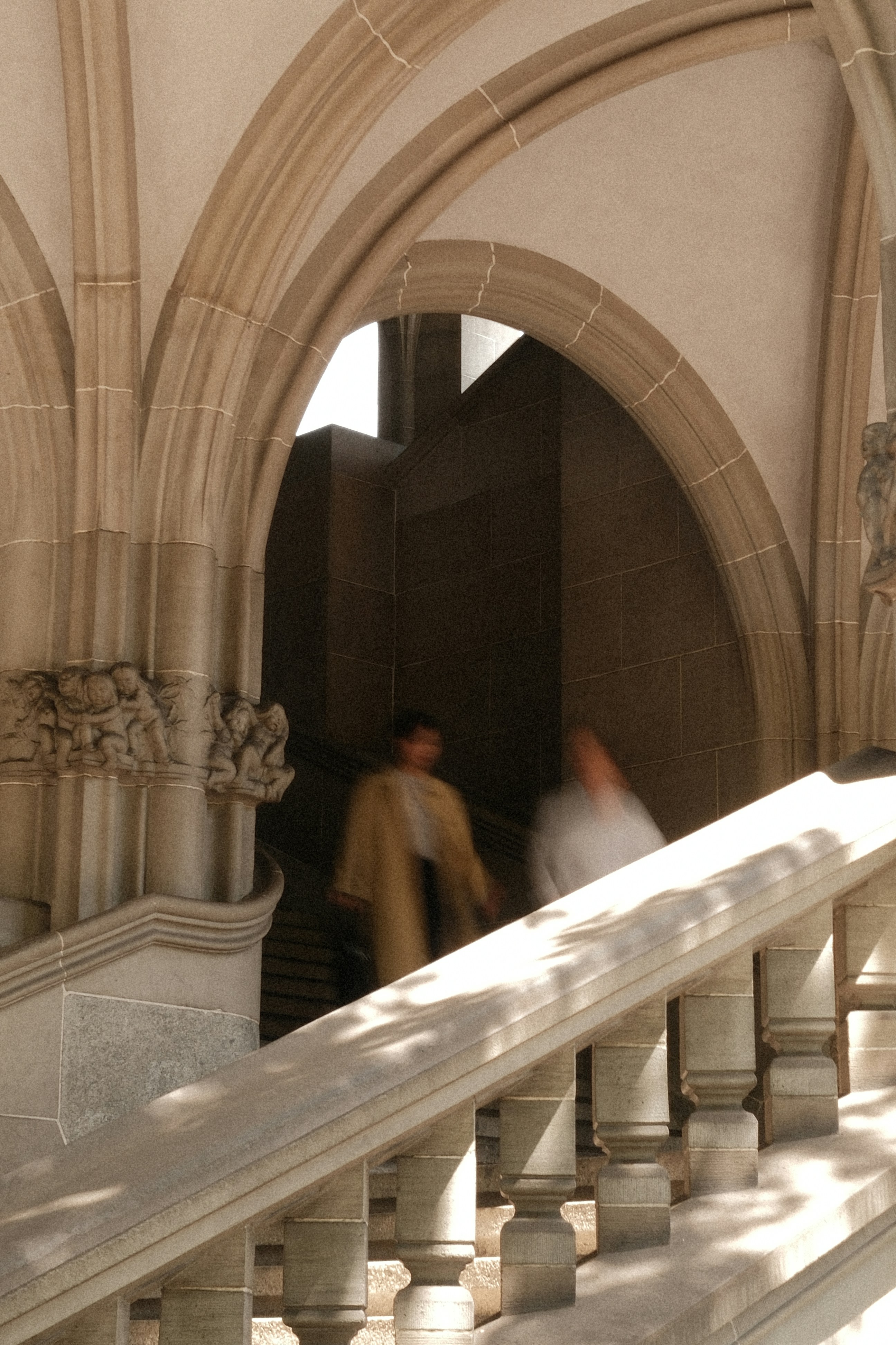 Stone arches and staircase with two blurry figures.