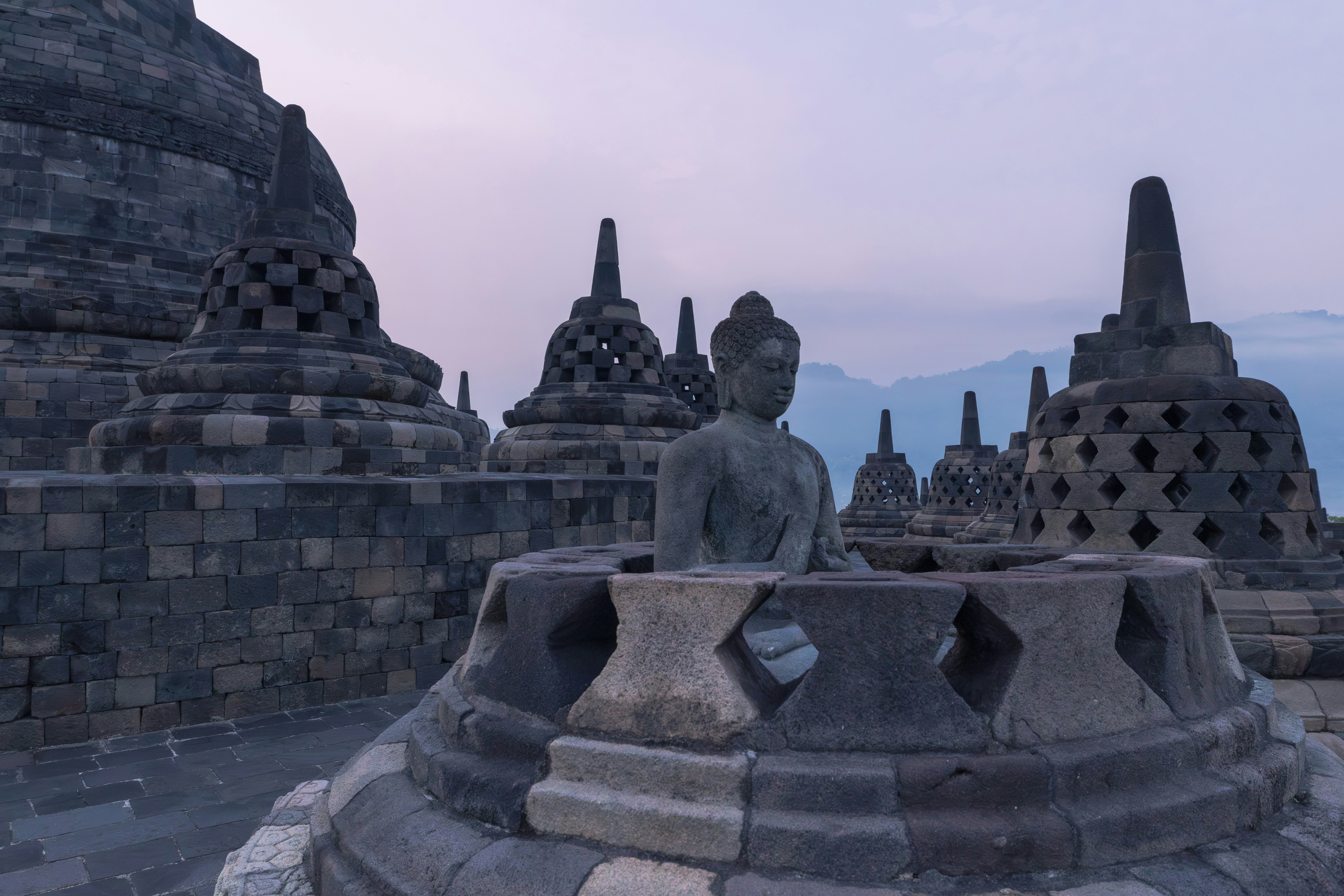 Stone buddha statue surrounded by ancient stupas at twilight.