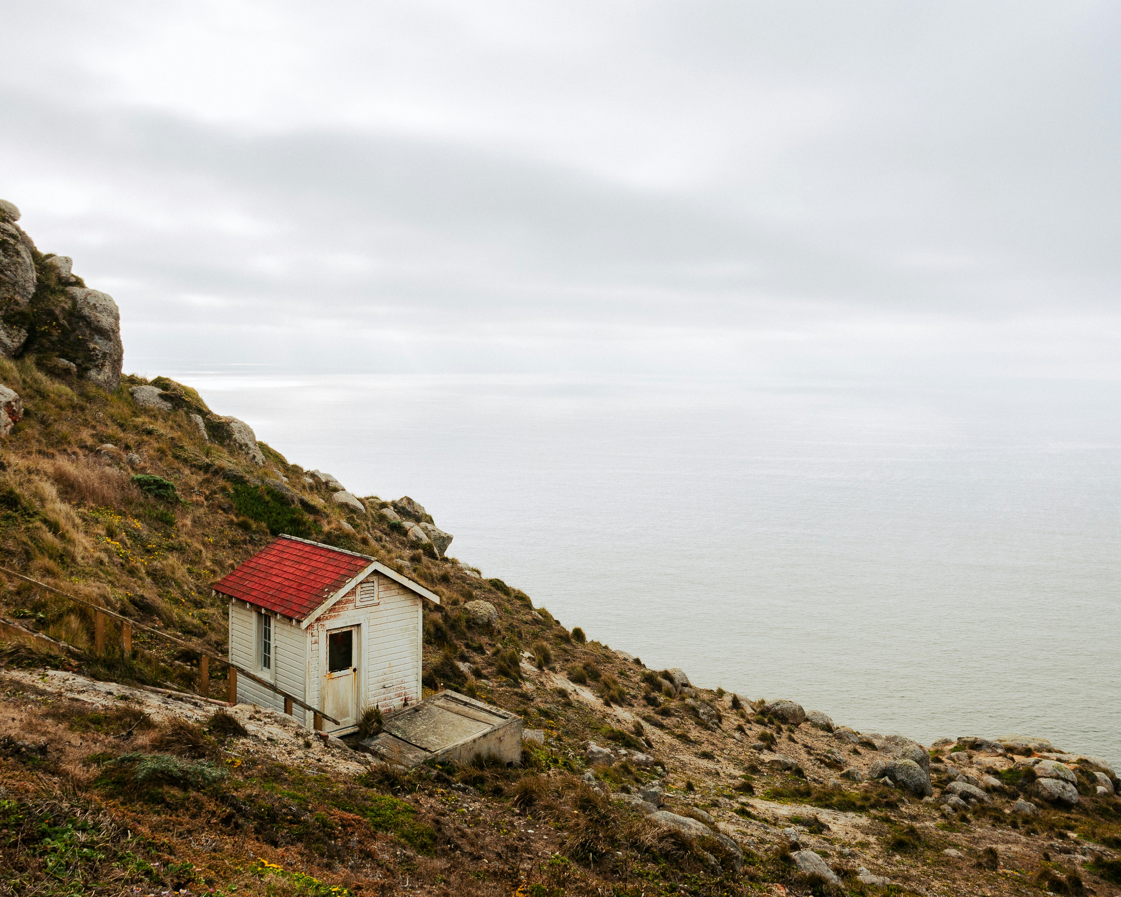 Red-roofed shack perched on the cliffside above a silent sea