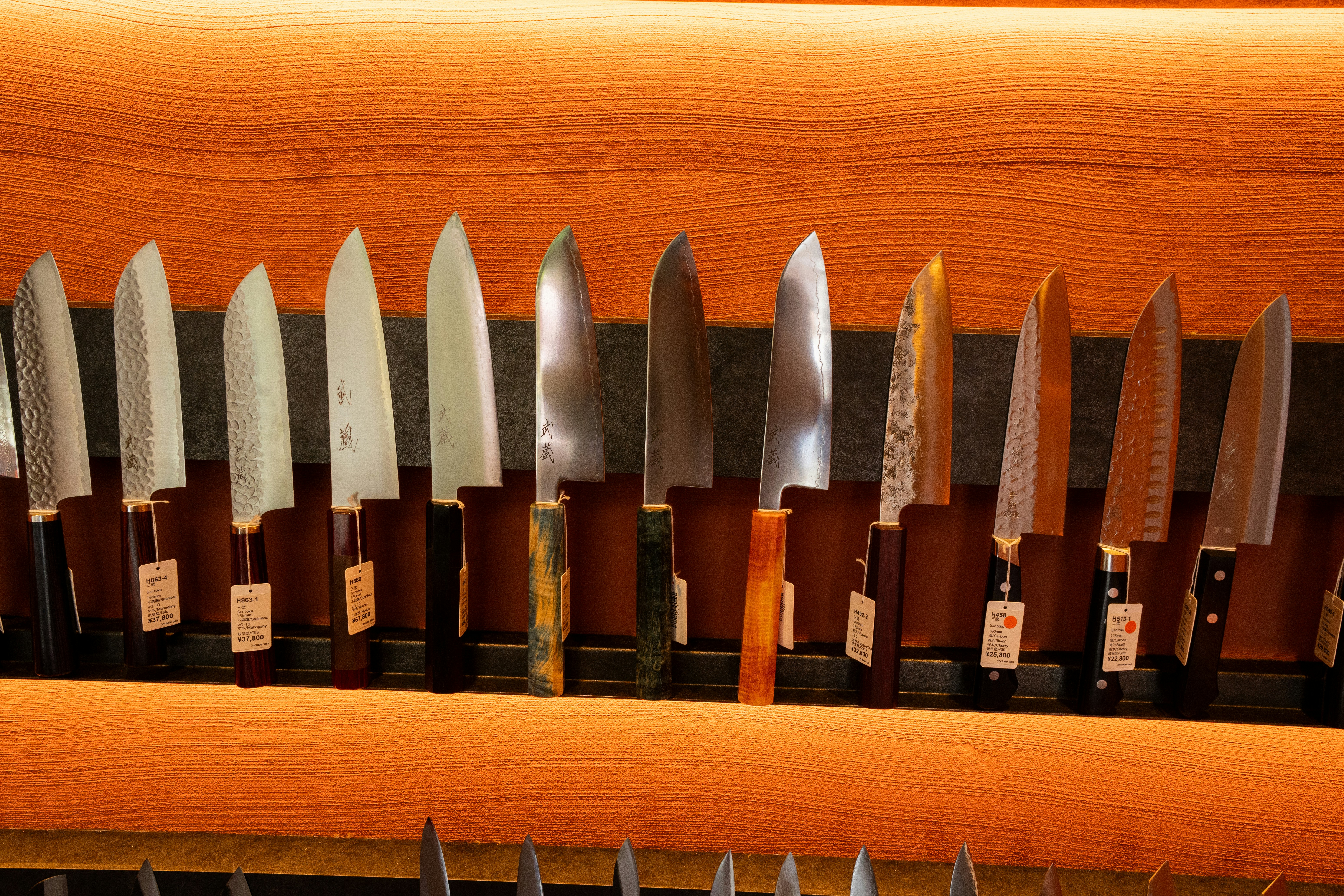 Row of polished kitchen knives glows under warm display lighting