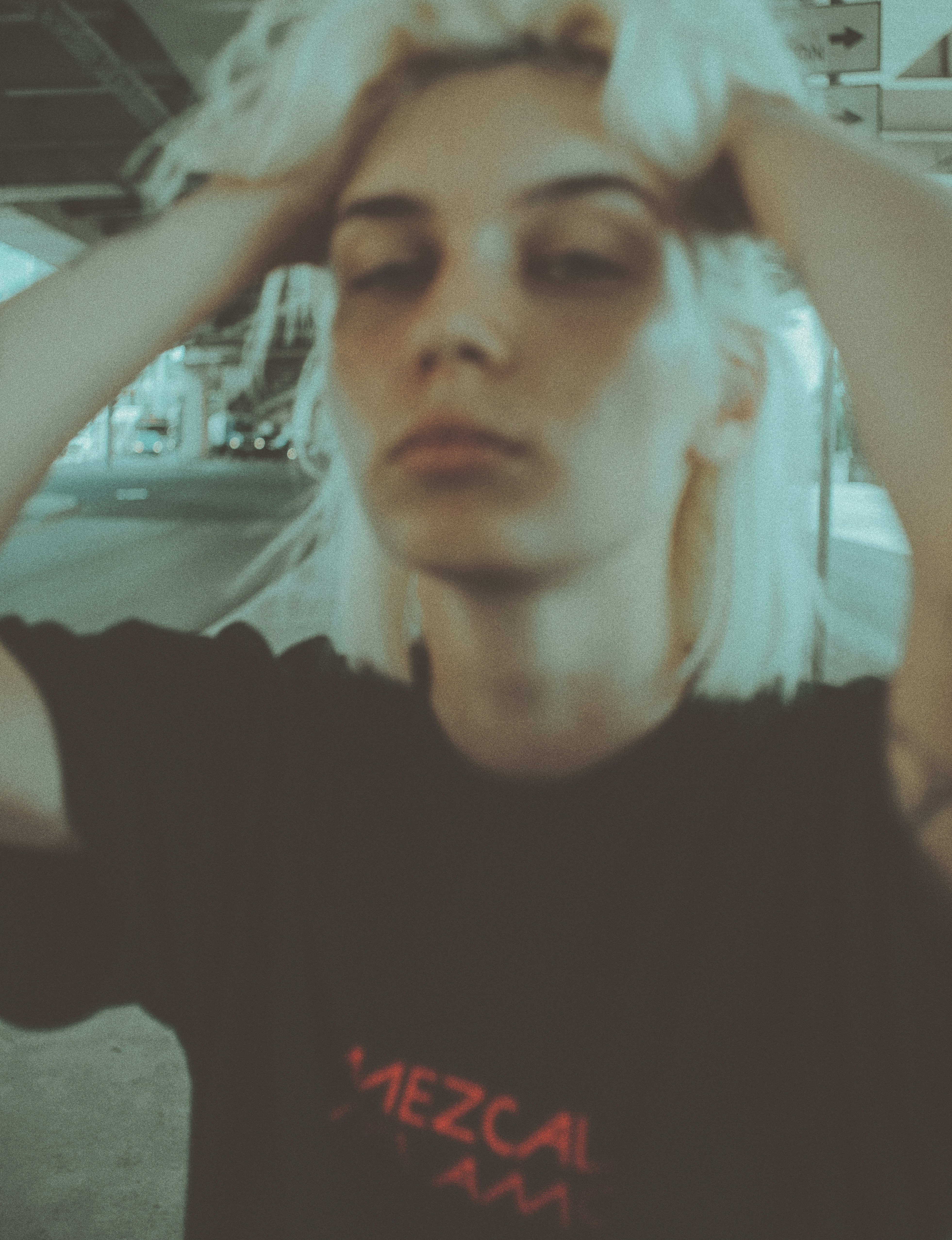 Blonde person with hands on head wearing dark t-shirt.