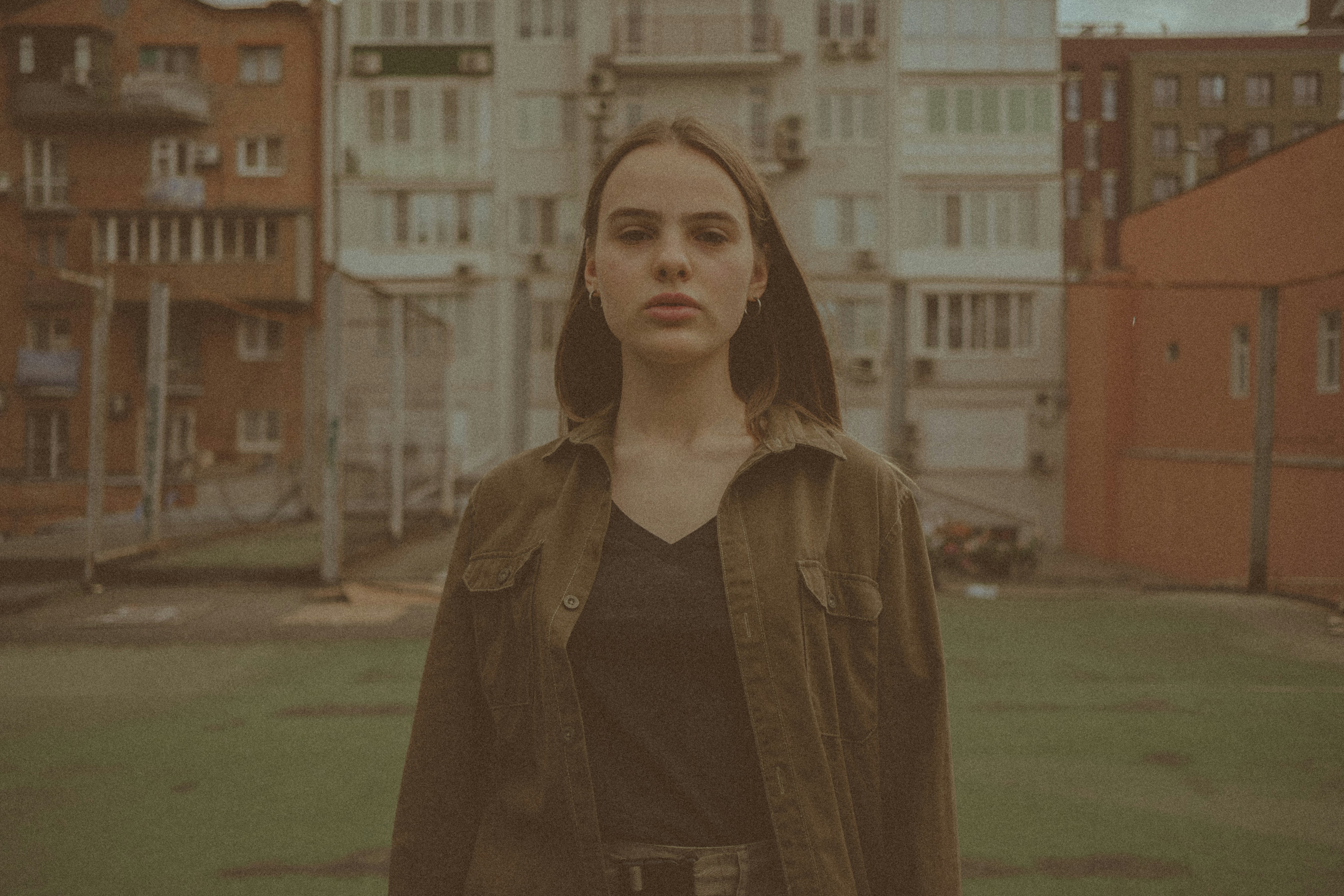 A young woman stands outdoors in front of residential buildings.