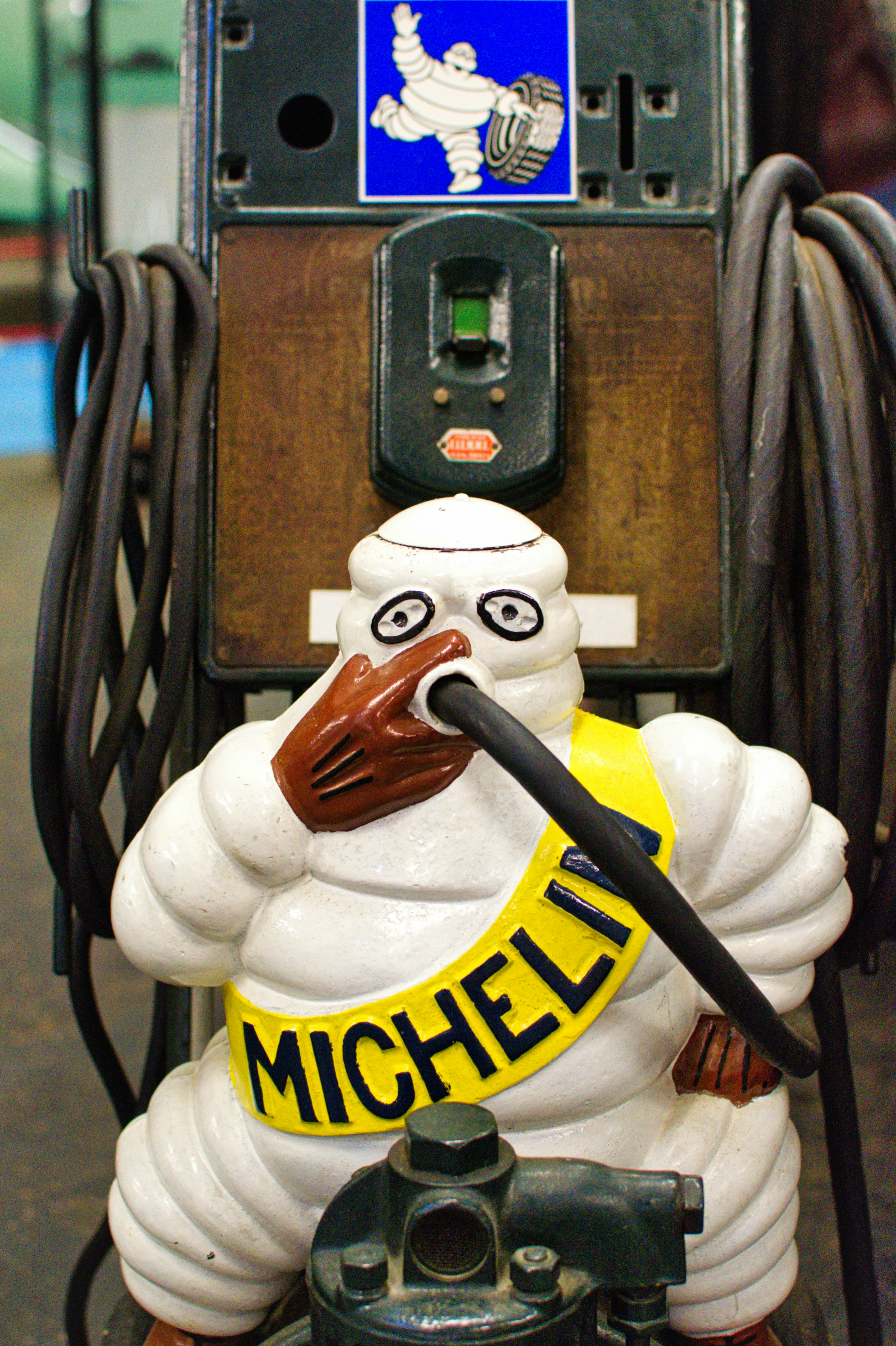Michelin Man with Hose: A Playful Siphon Gesture in a Retro Gas Station Scene
