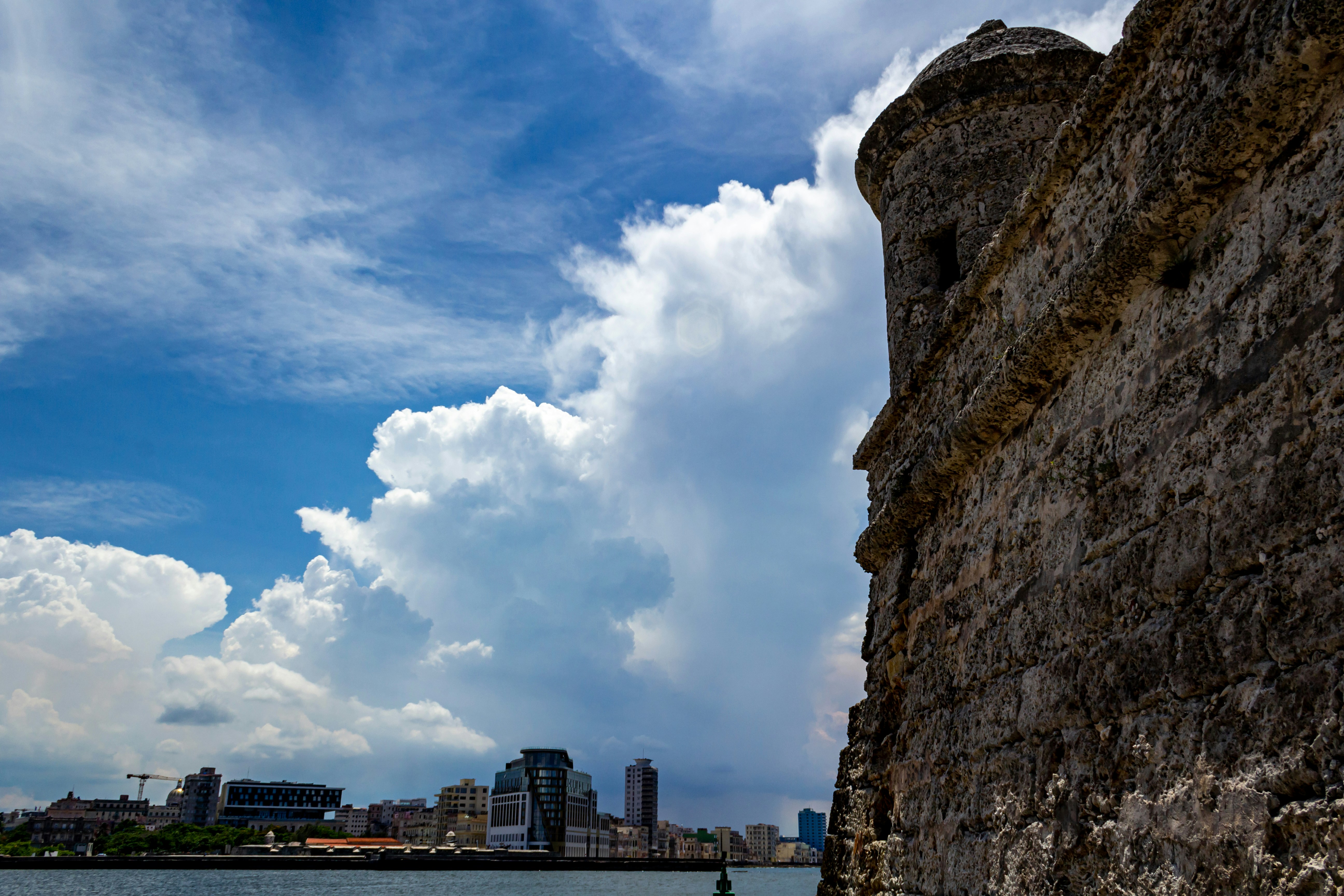 Stone fortress wall dominates the right, with a skyline and river on the left under a vivid blue sky with clouds.