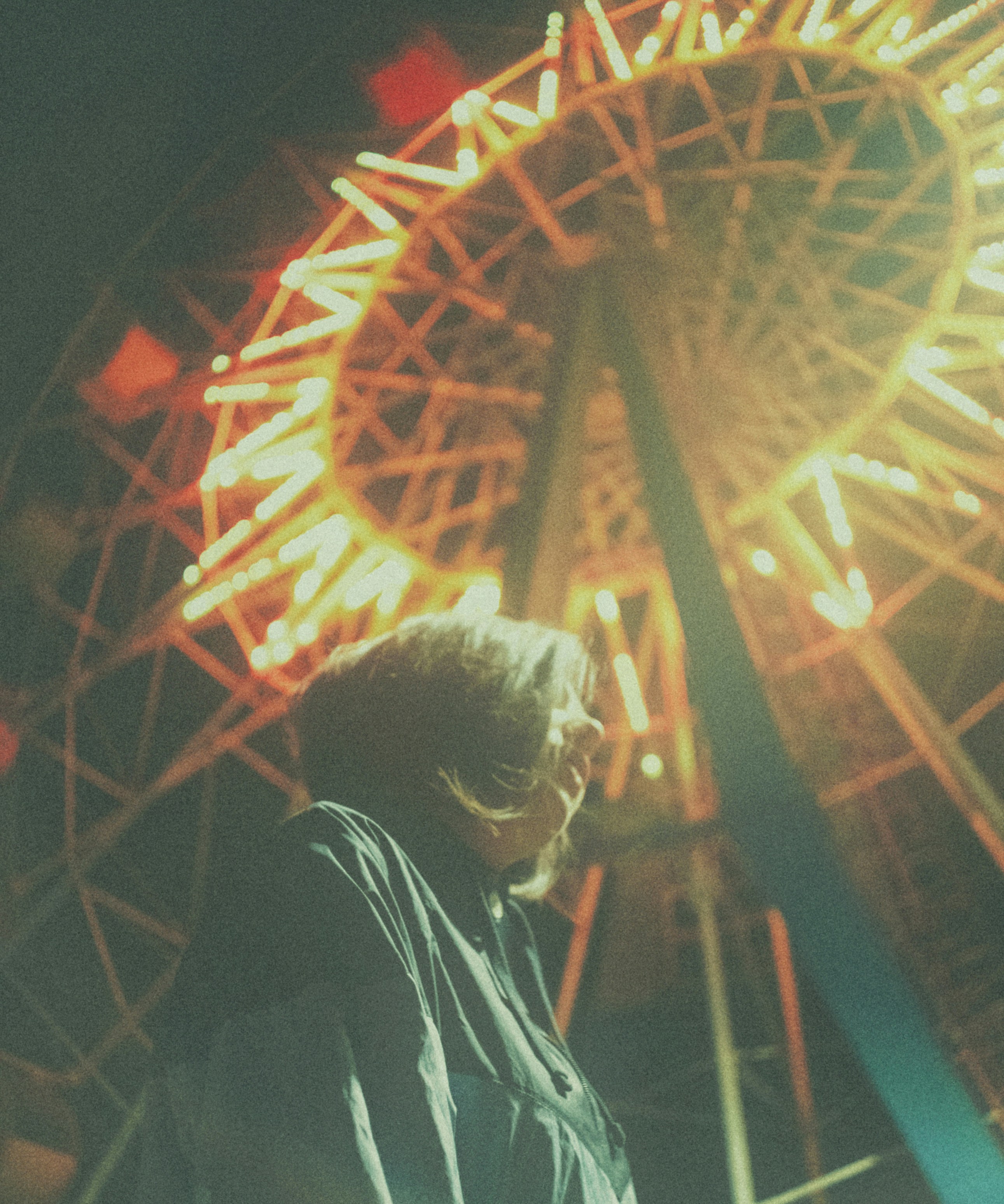 Neon Wheelkeeper: A Quiet Portrait Beneath Pulsing Ferris Lights