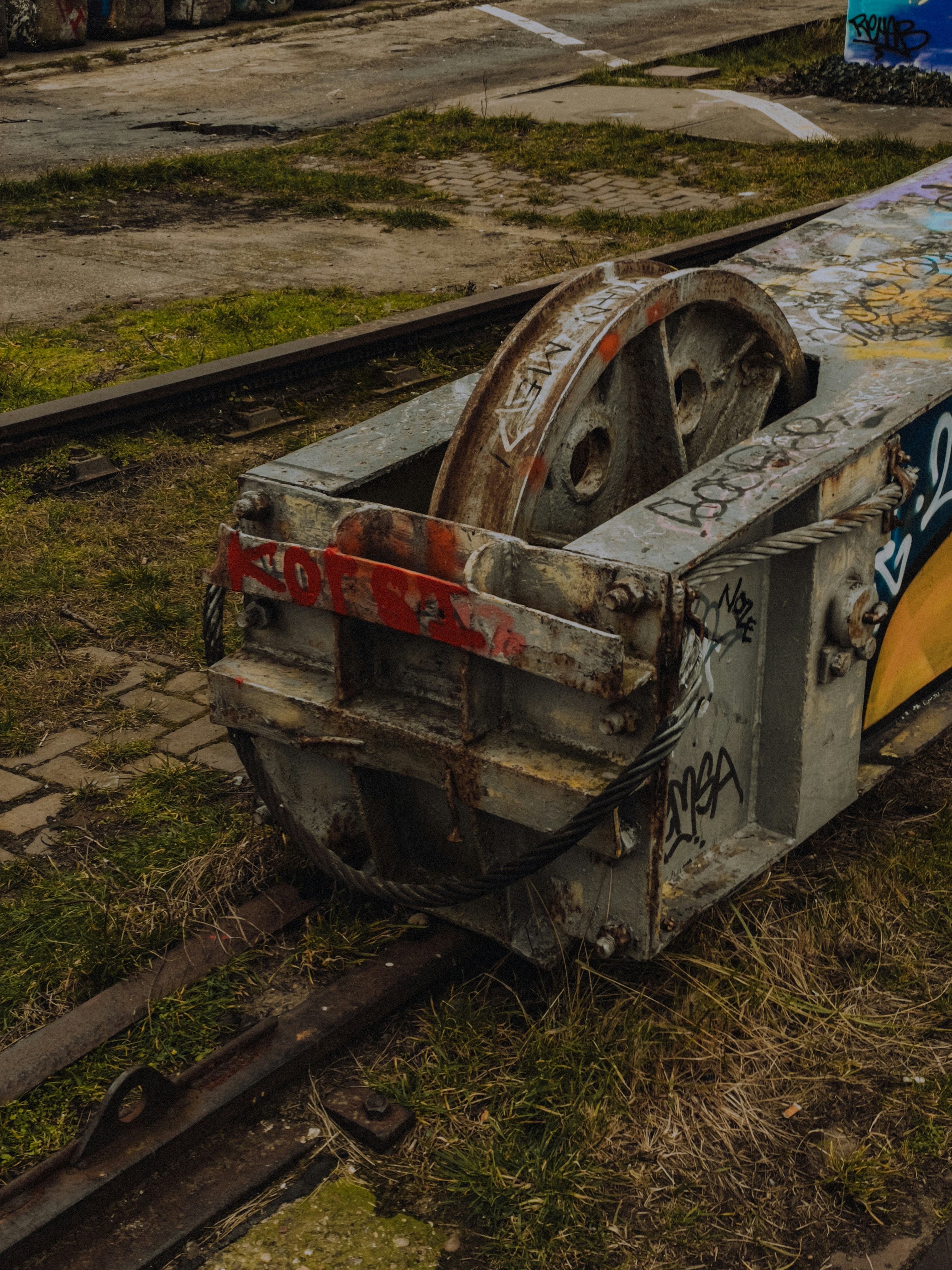 Graffiti-covered industrial wheel resting on abandoned train tracks.