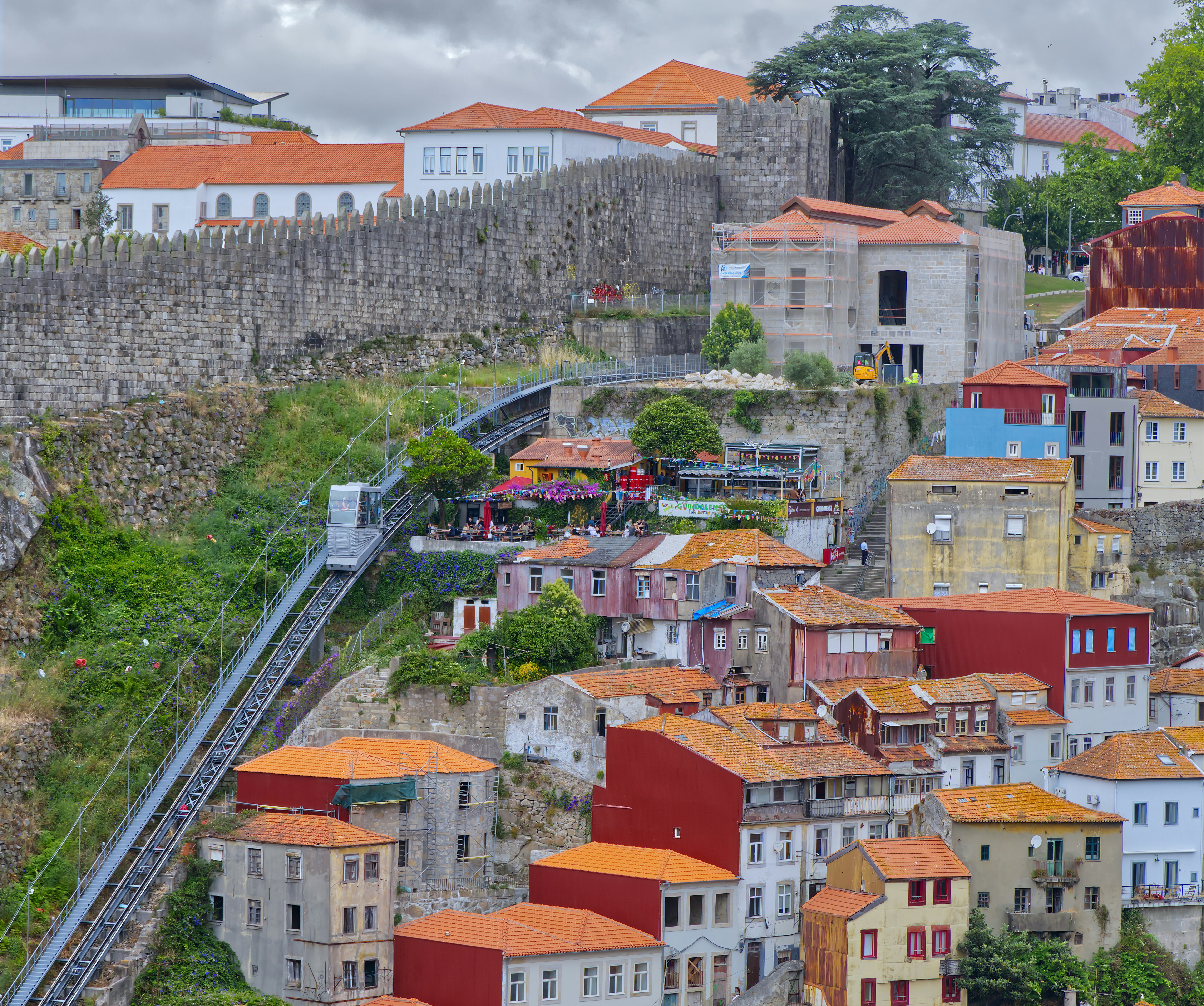 Le funiculaire de Porto, une ascension poétique entre pierre et couleurs. Accroché à la colline, le funiculaire trace sa ligne au cœur d’un dédale de maisons aux toits de tuiles rouges, empilées comme des cubes. Les murs de pierre, les escaliers sinueux, la terrasse d’un restaurant et les touches de végétation sauvage encadrent cette remontée mécanique, offrant un spectacle où le moderne dialogue avec l’authentique. En haut, les remparts médiévaux veillent sur la ville, tandis qu’en bas, la vie s’anime dans les ruelles et les terrasses ombragées.