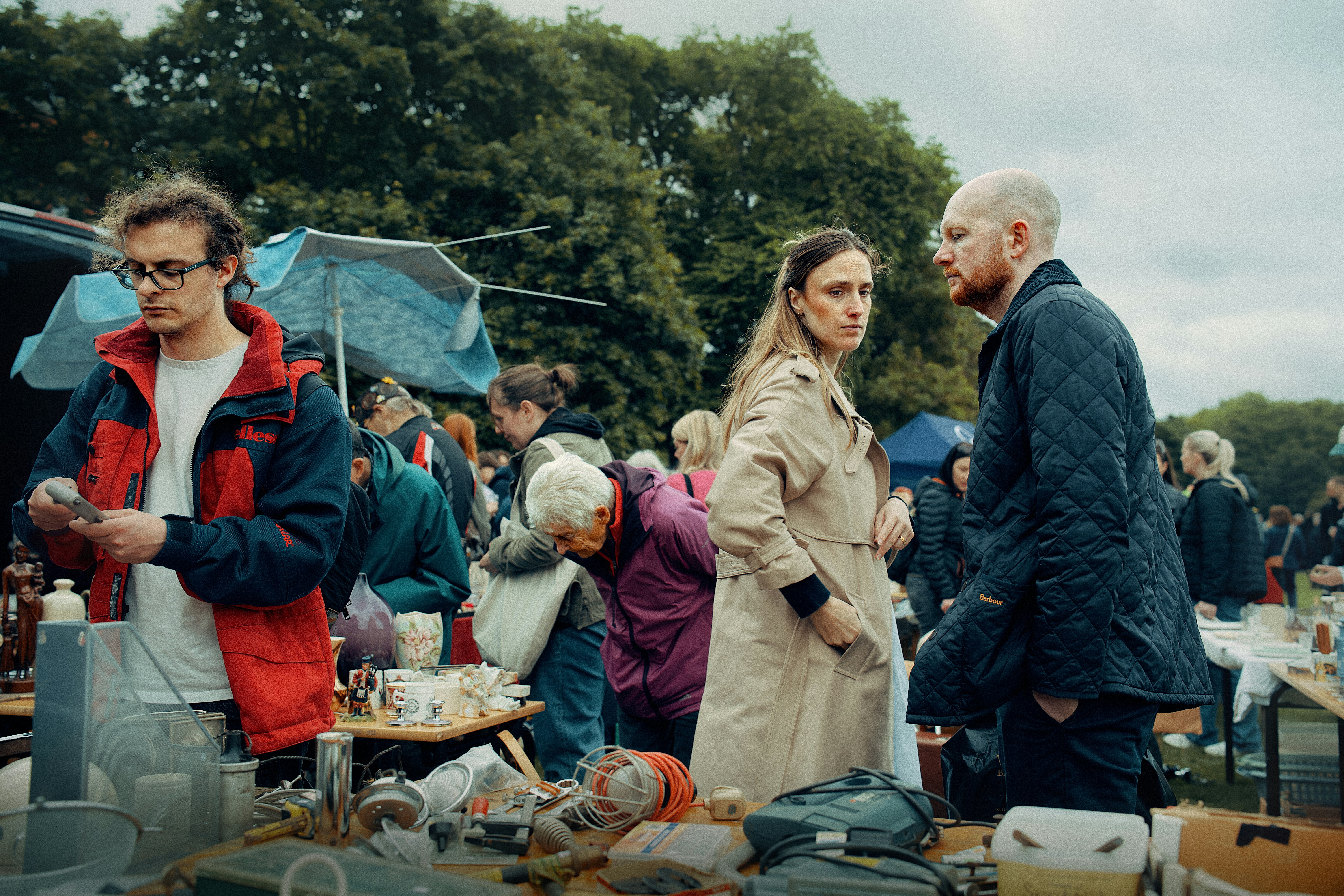 Two strangers in a bustling outdoor market pause amid a sea of devices and trinkets