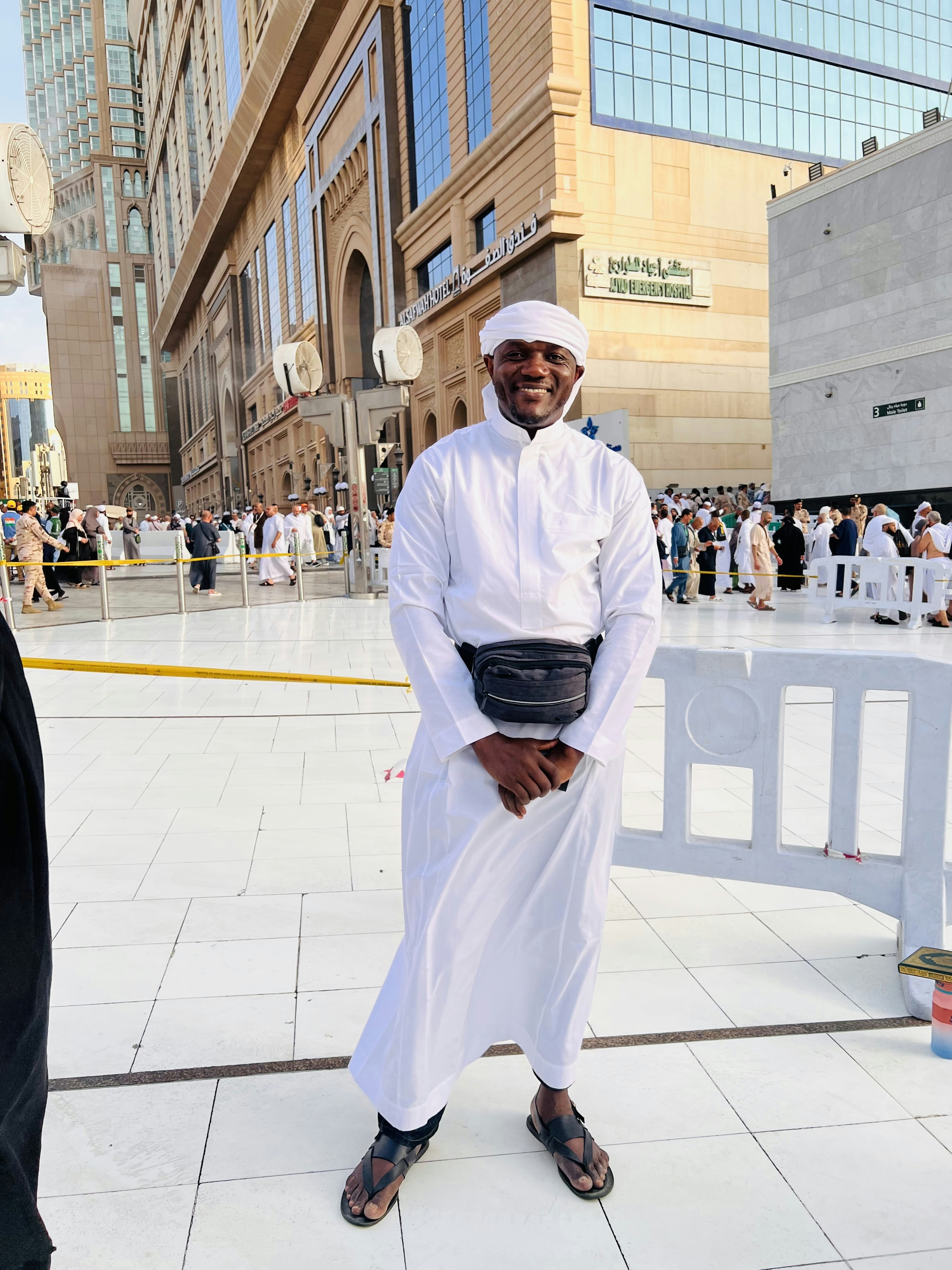 White-robed pilgrim posing in a sunlit plaza before a grand mosque