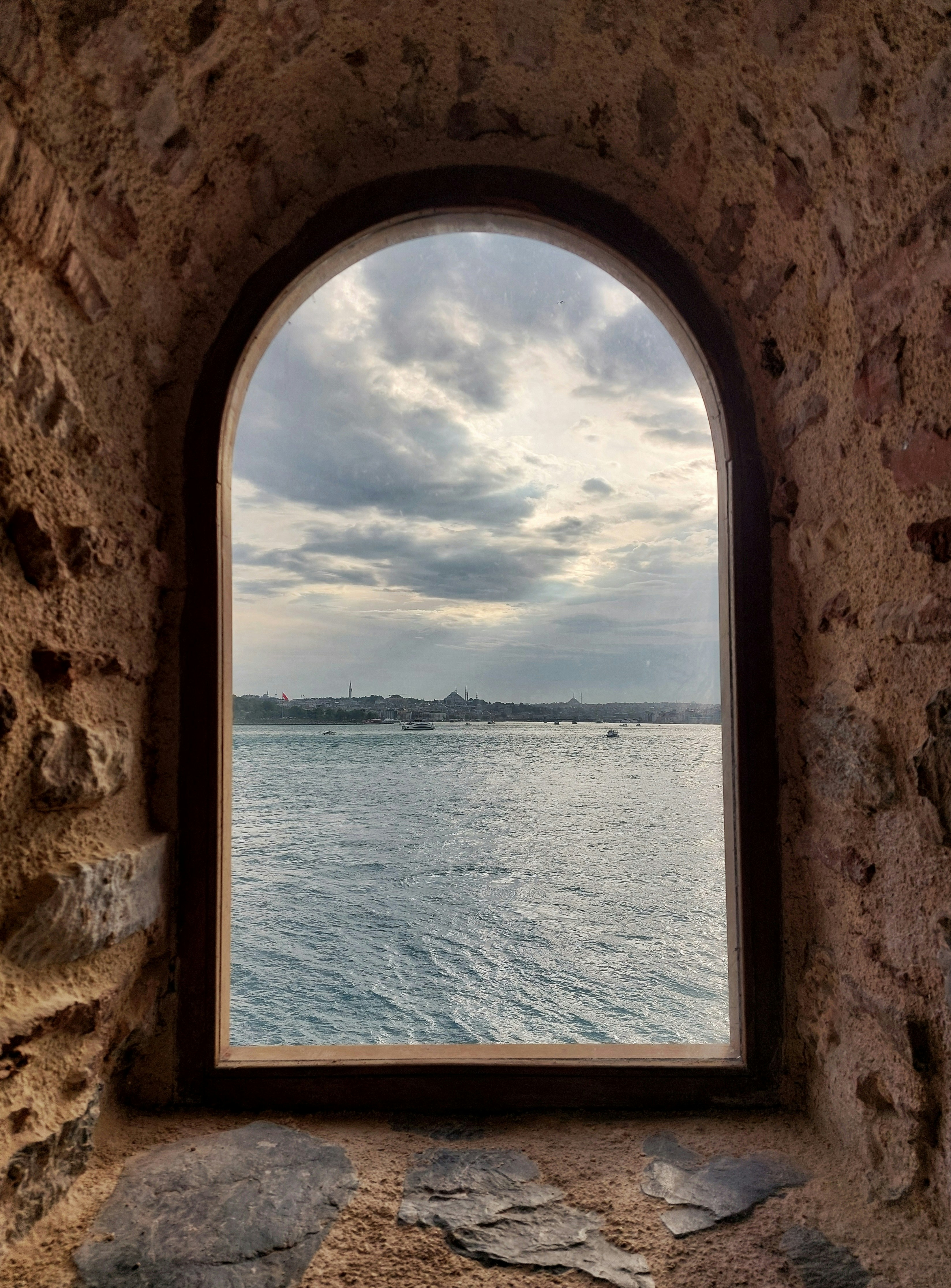 View of a cloudy sea through an arched stone window.